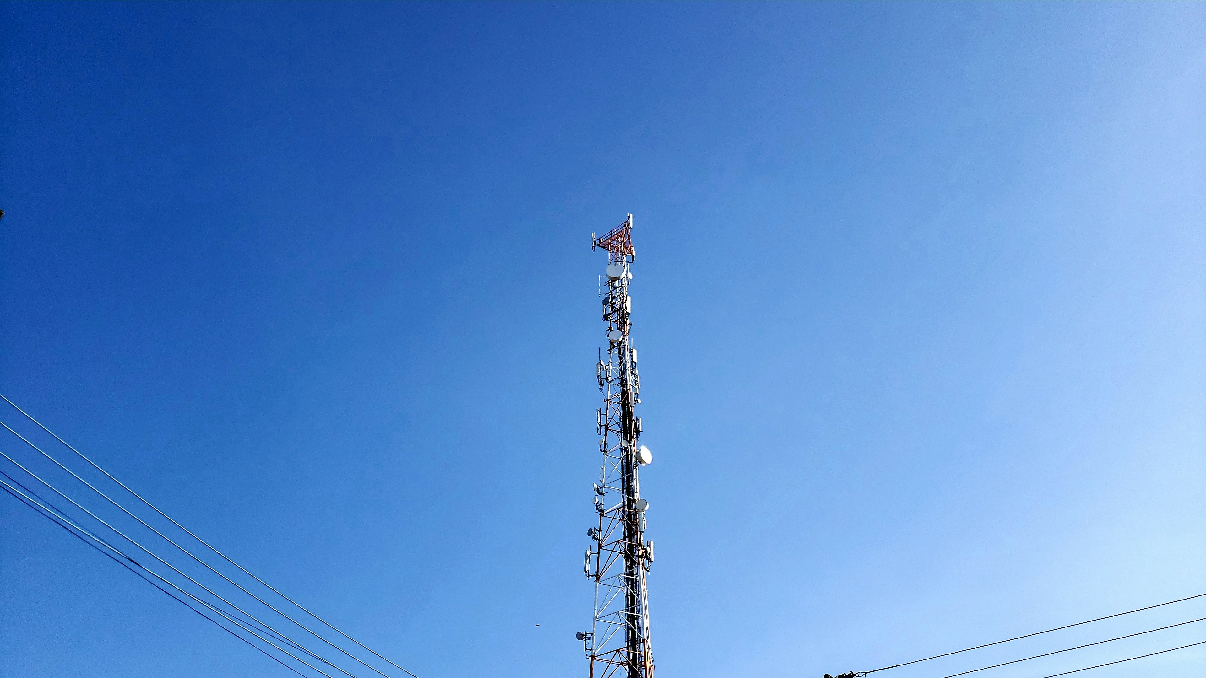 Tall electric tower against a clear blue sky with power lines extending outward.