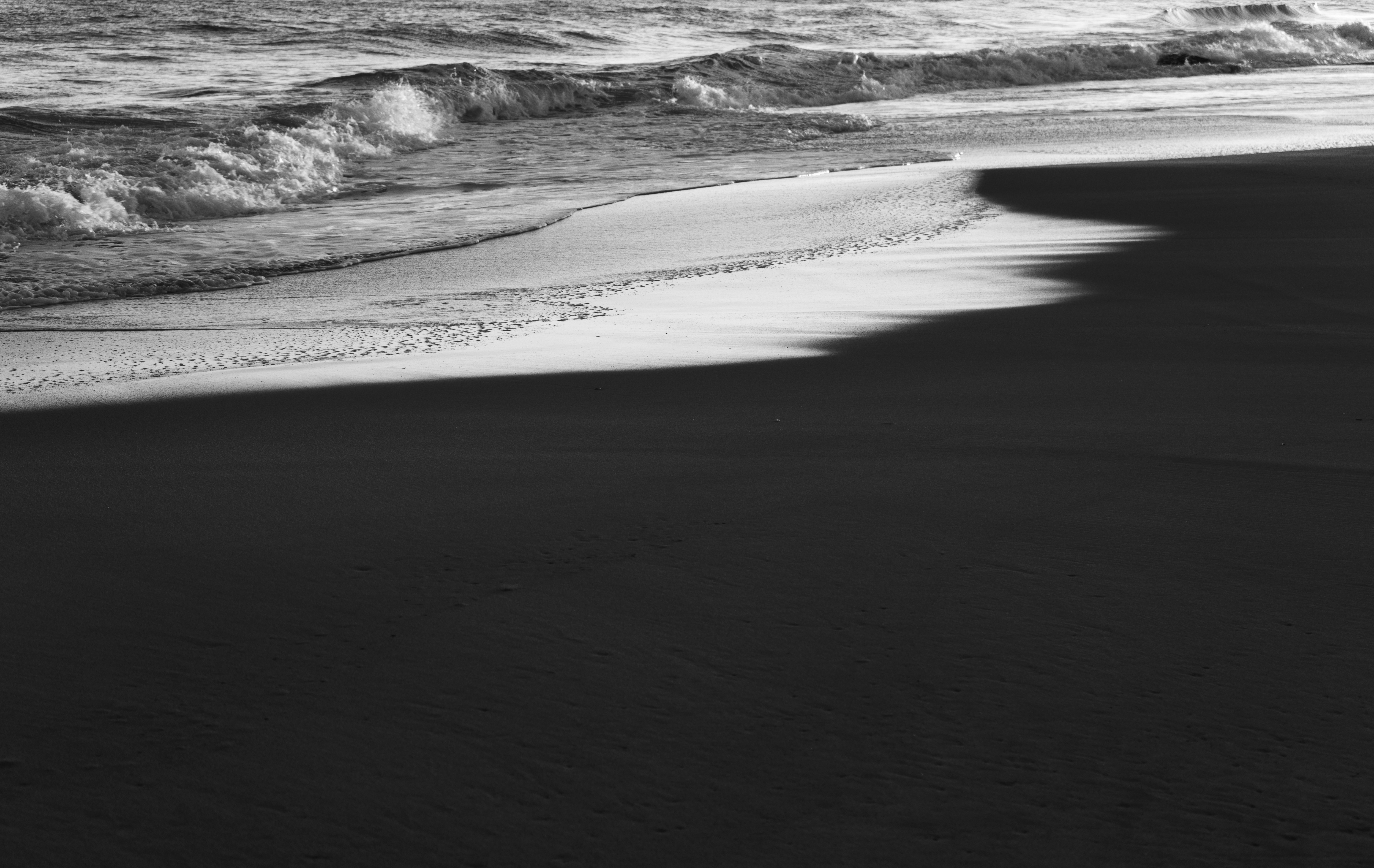 Black and white shoreline with gentle waves meeting dark sand.