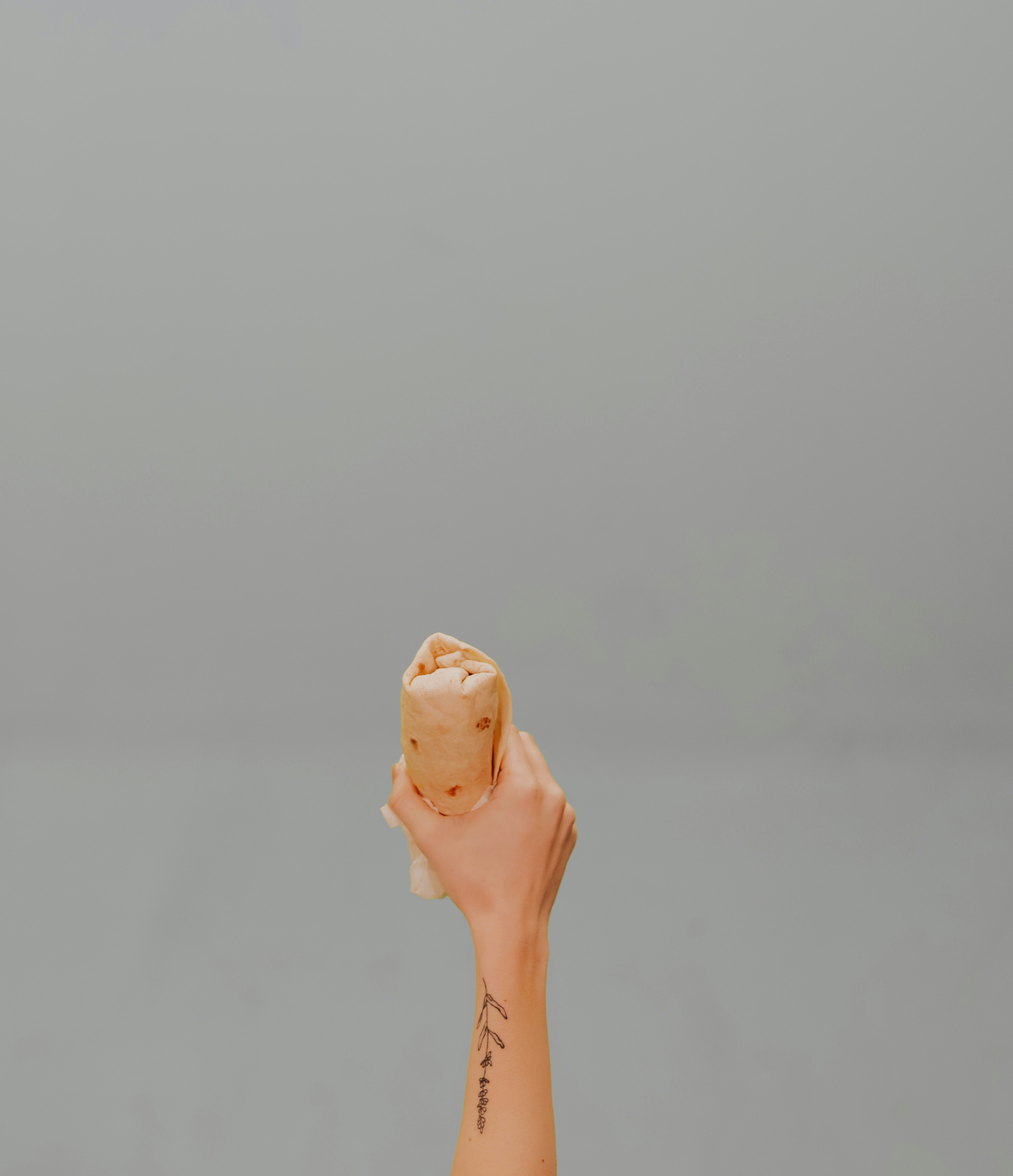 Hand holding a wrapped burrito against a soft gray background, emphasizing the connection between food and personal expression.