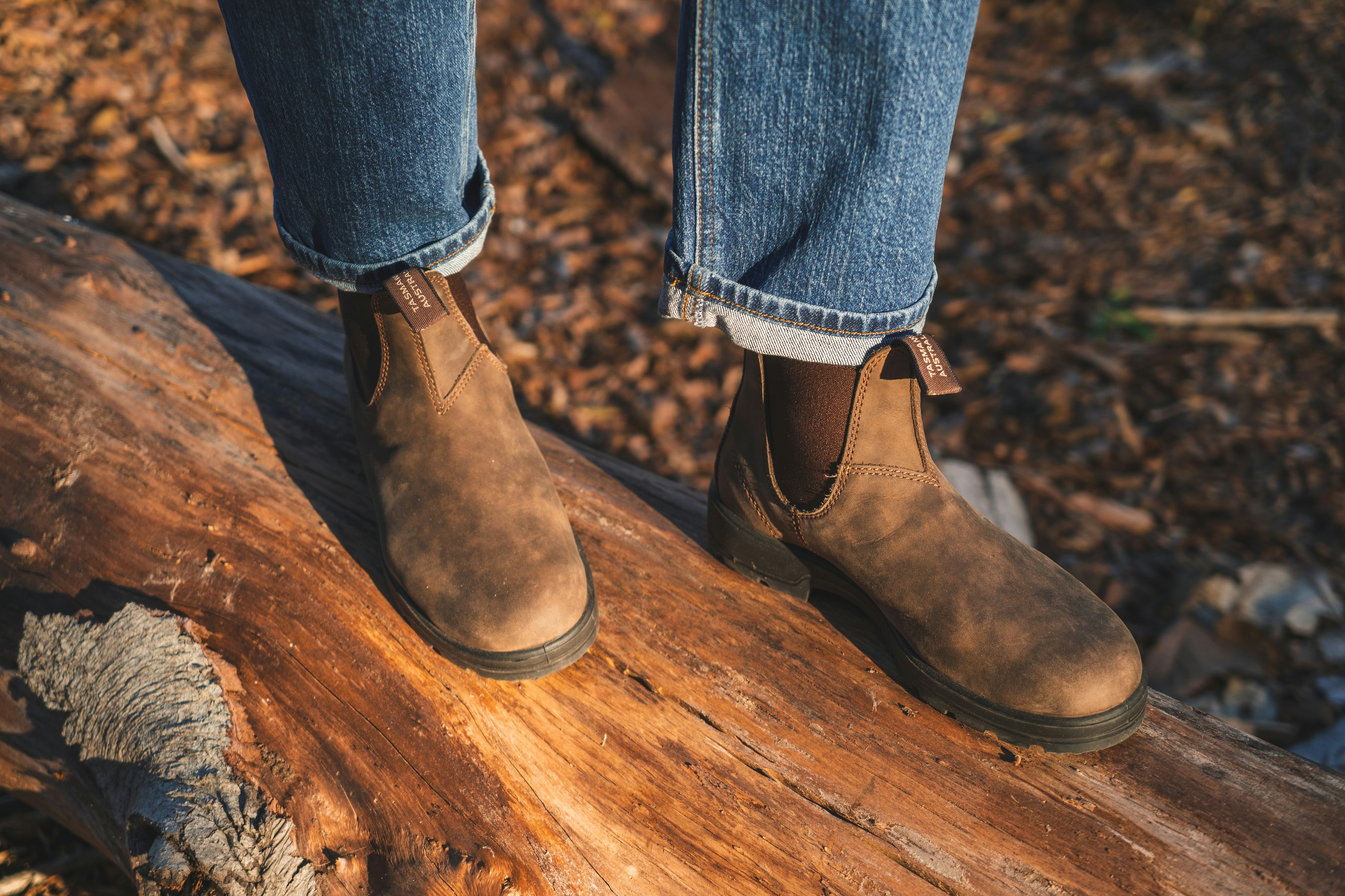Worn leather boots standing on a sunlit log surrounded by autumn leaves.