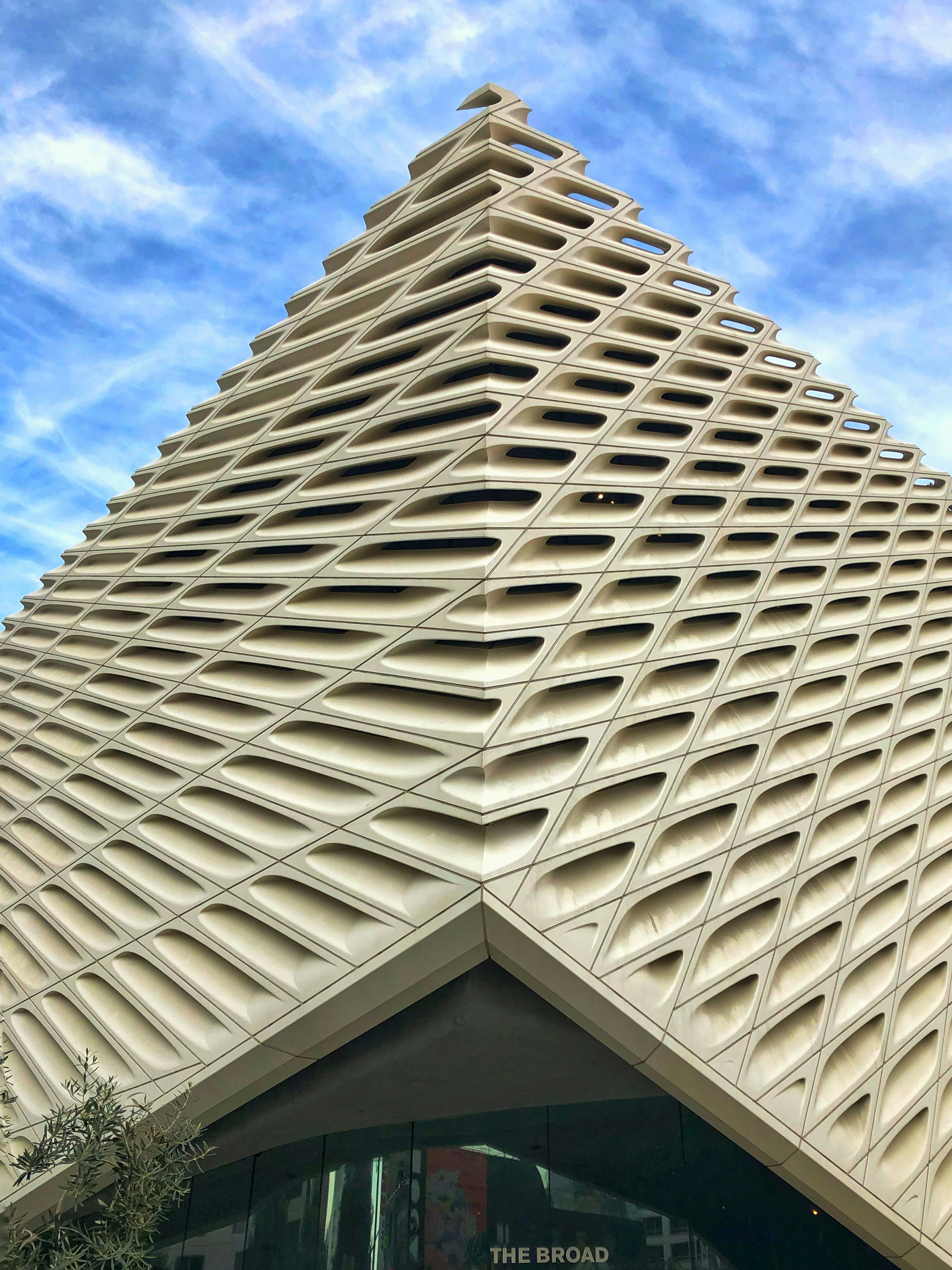 Angular facade of The Broad museum showcasing intricate lattice design against a blue sky. The structure's unique geometry draws the eye upward.