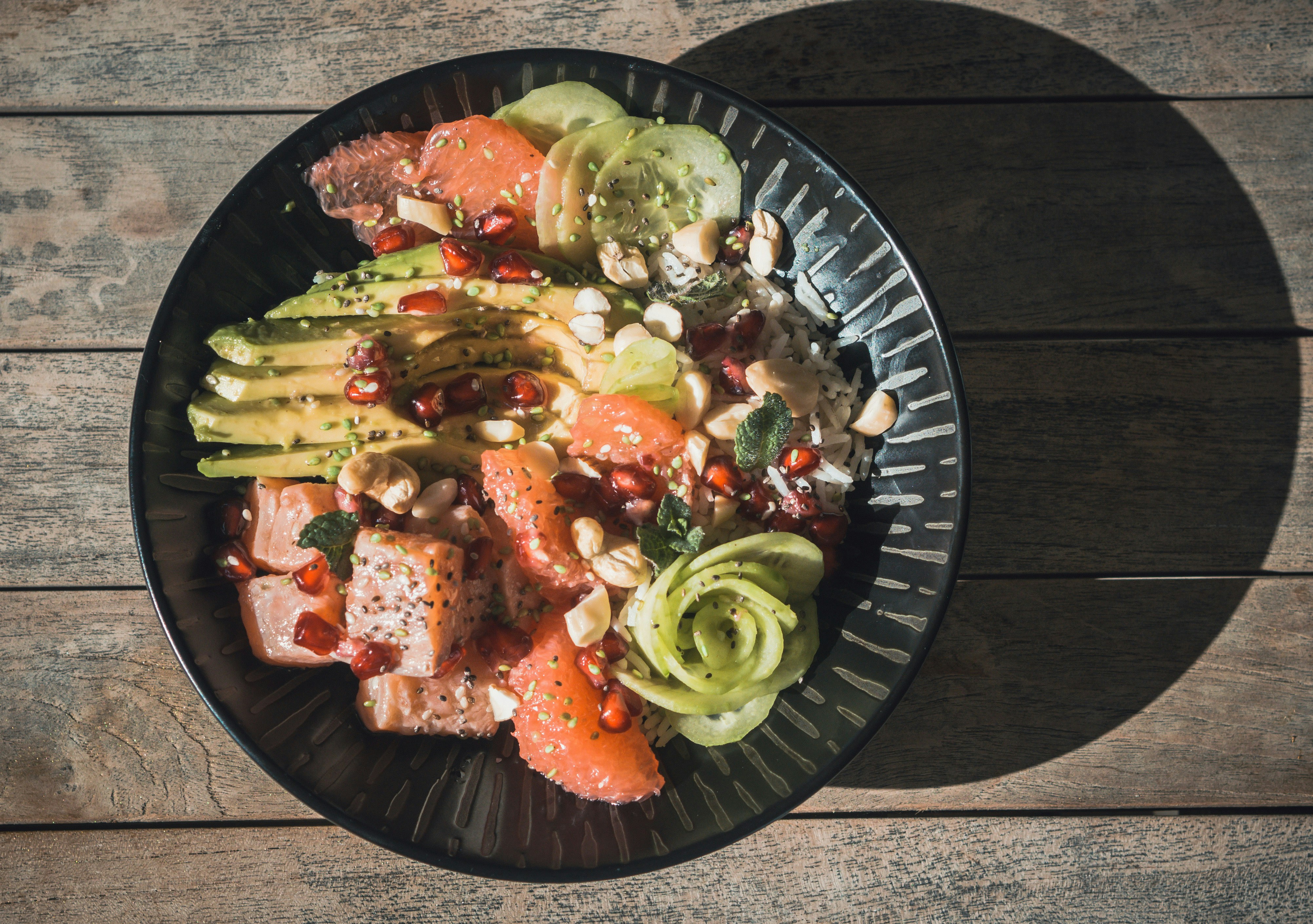 A colorful bowl featuring salmon, avocado, and fresh vegetables garnished with nuts and herbs. The arrangement emphasizes texture and freshness.