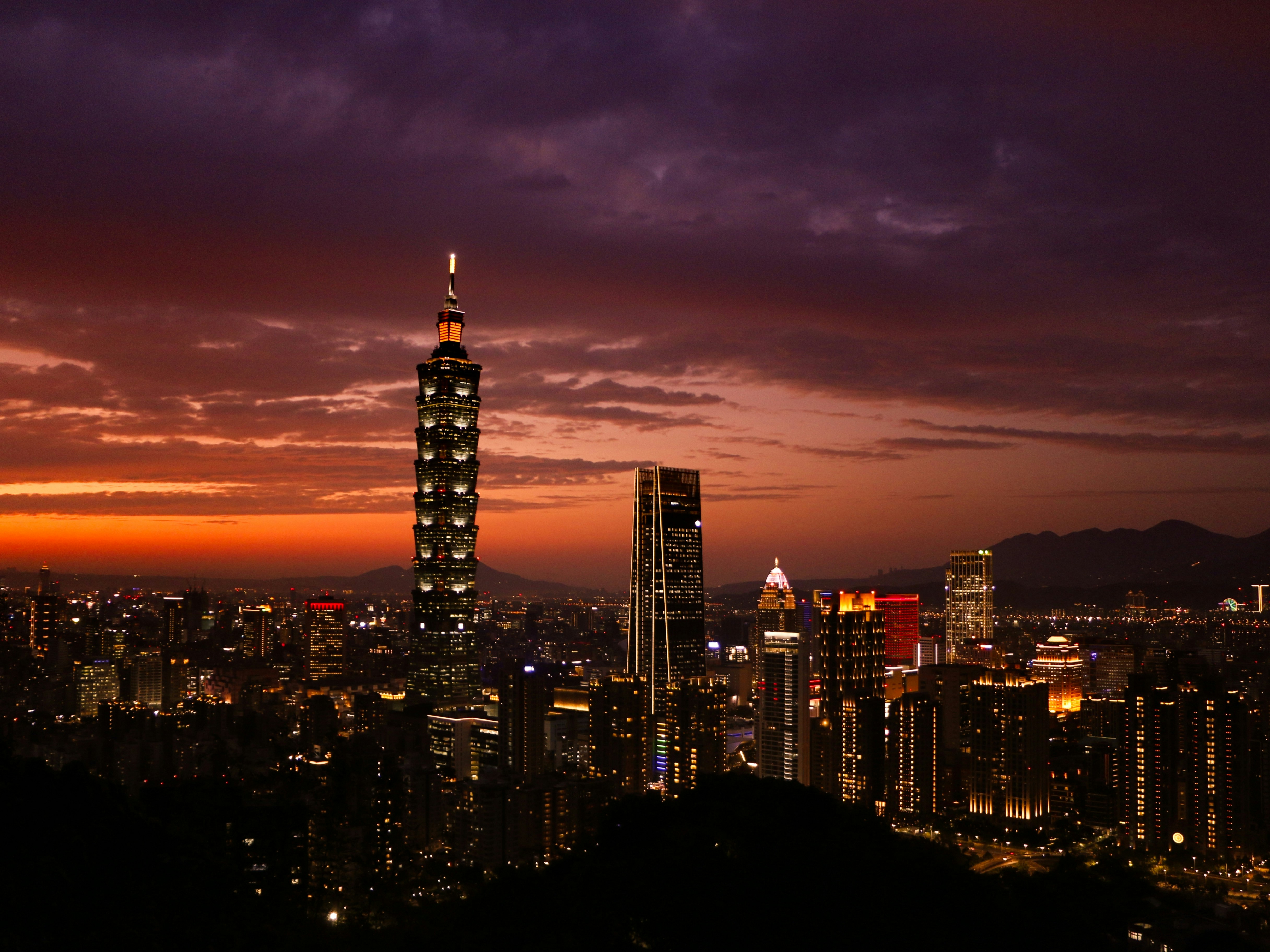 Taipei skyline illuminated at dusk, featuring iconic skyscrapers against a vibrant sunset sky.
