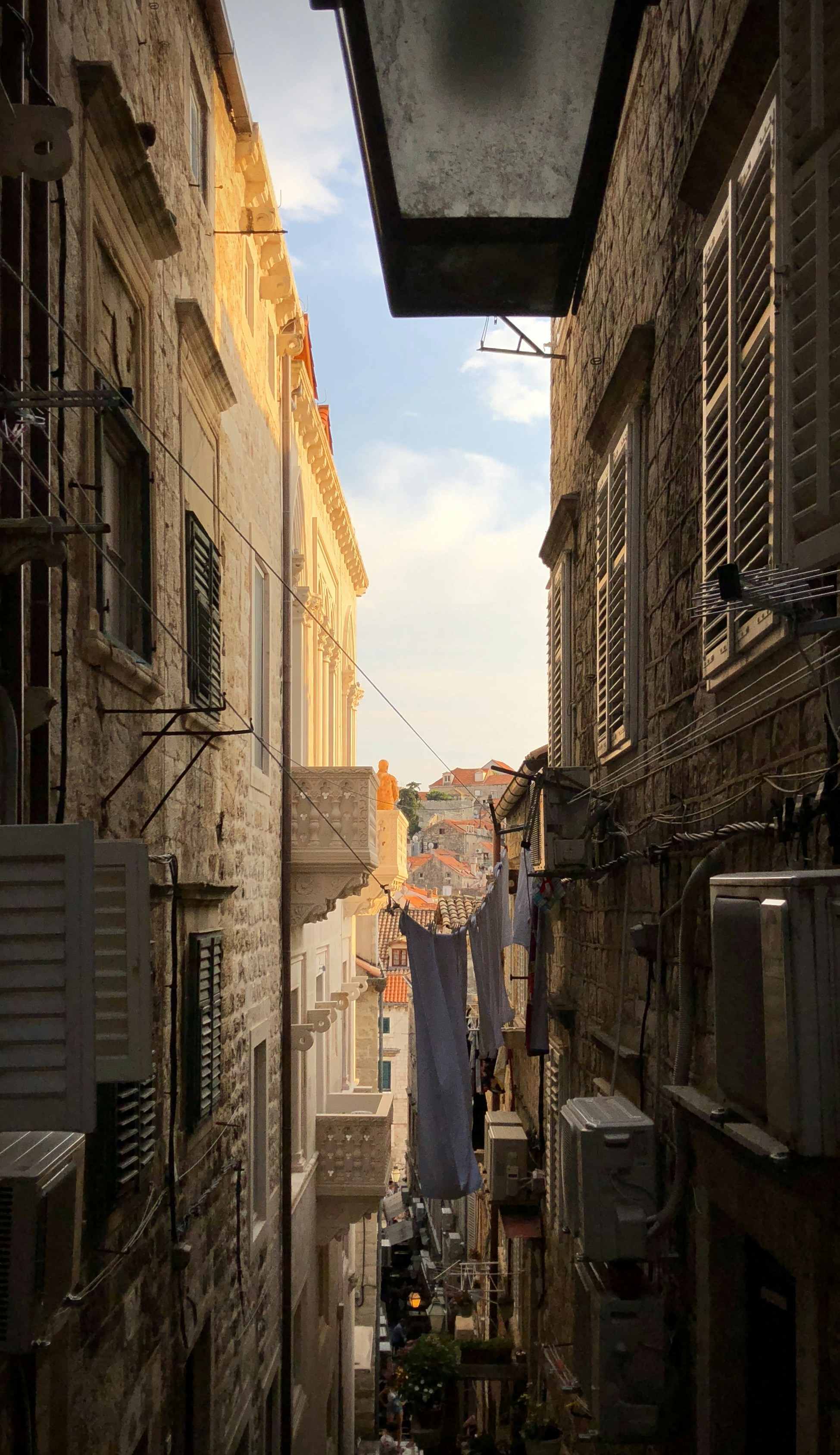 Narrow alleyway in a historic town with buildings on either side and laundry hanging between them. Warm light filters through, illuminating the scene.