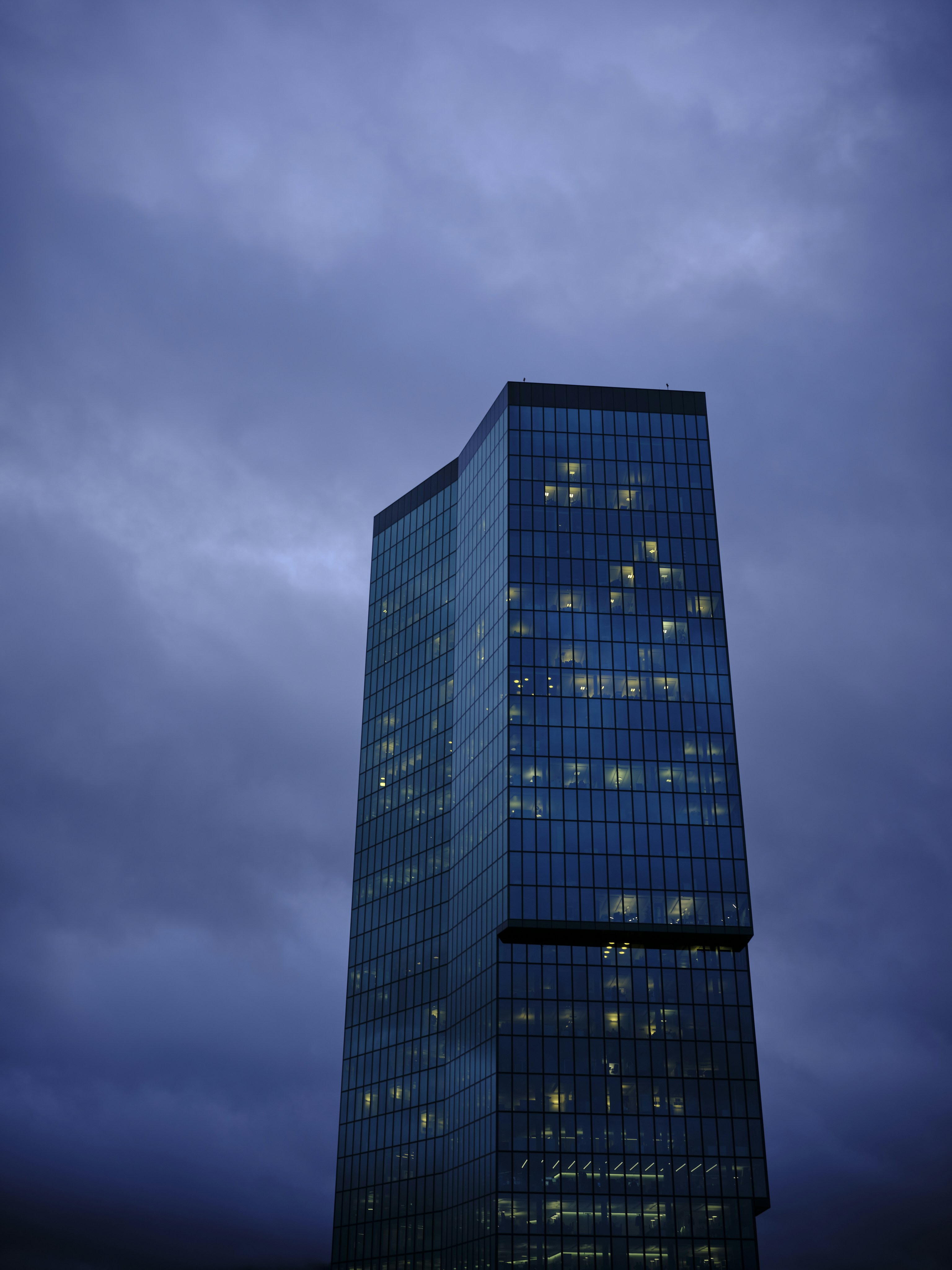 A modern glass skyscraper illuminated against a dramatic twilight sky, showcasing the interplay of light and architecture.