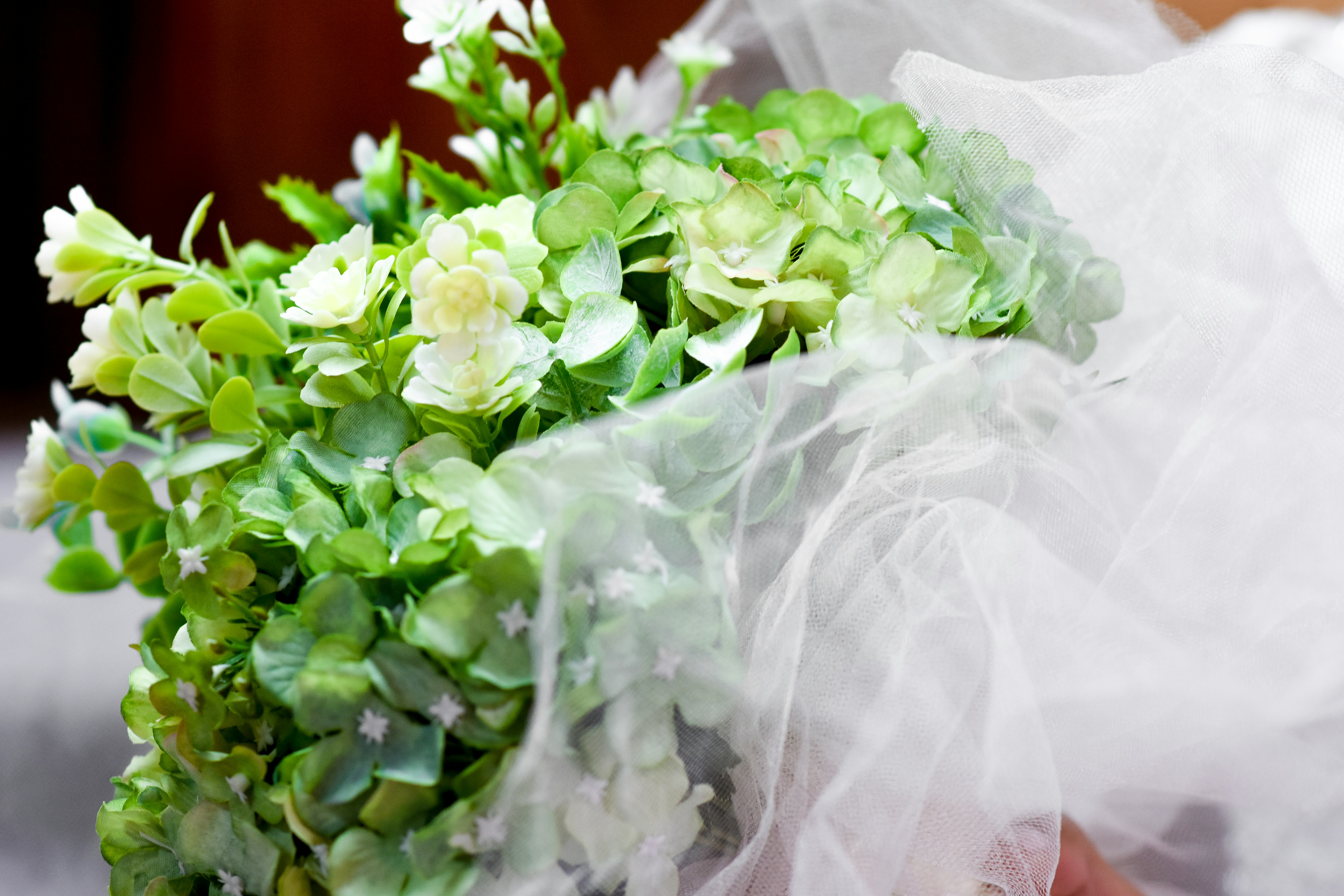 Delicate bouquet of green and white flowers wrapped in soft tulle, showcasing intricate details and textures.