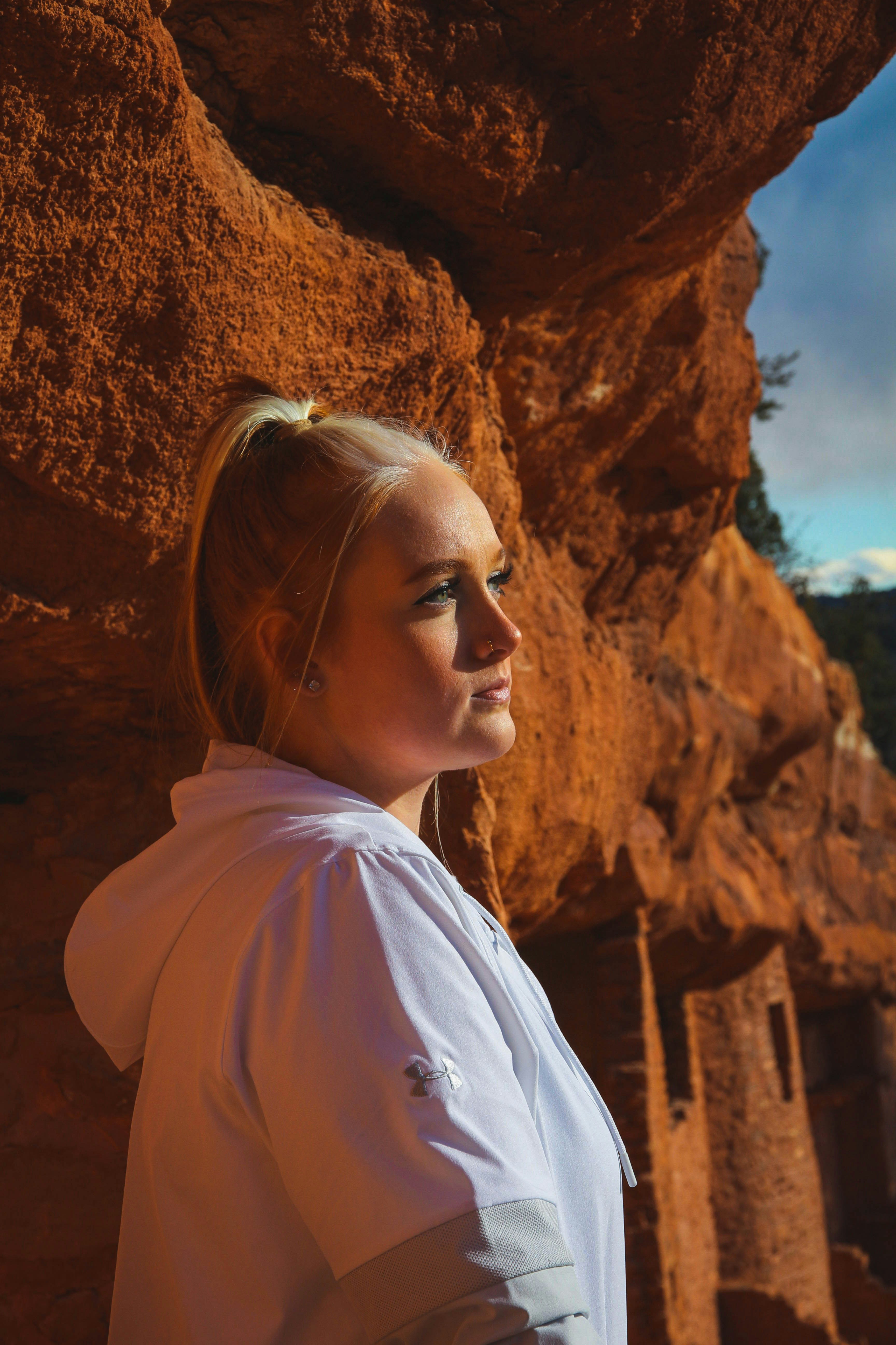 Woman in white shirt standing near brown rock formation during daytime ...