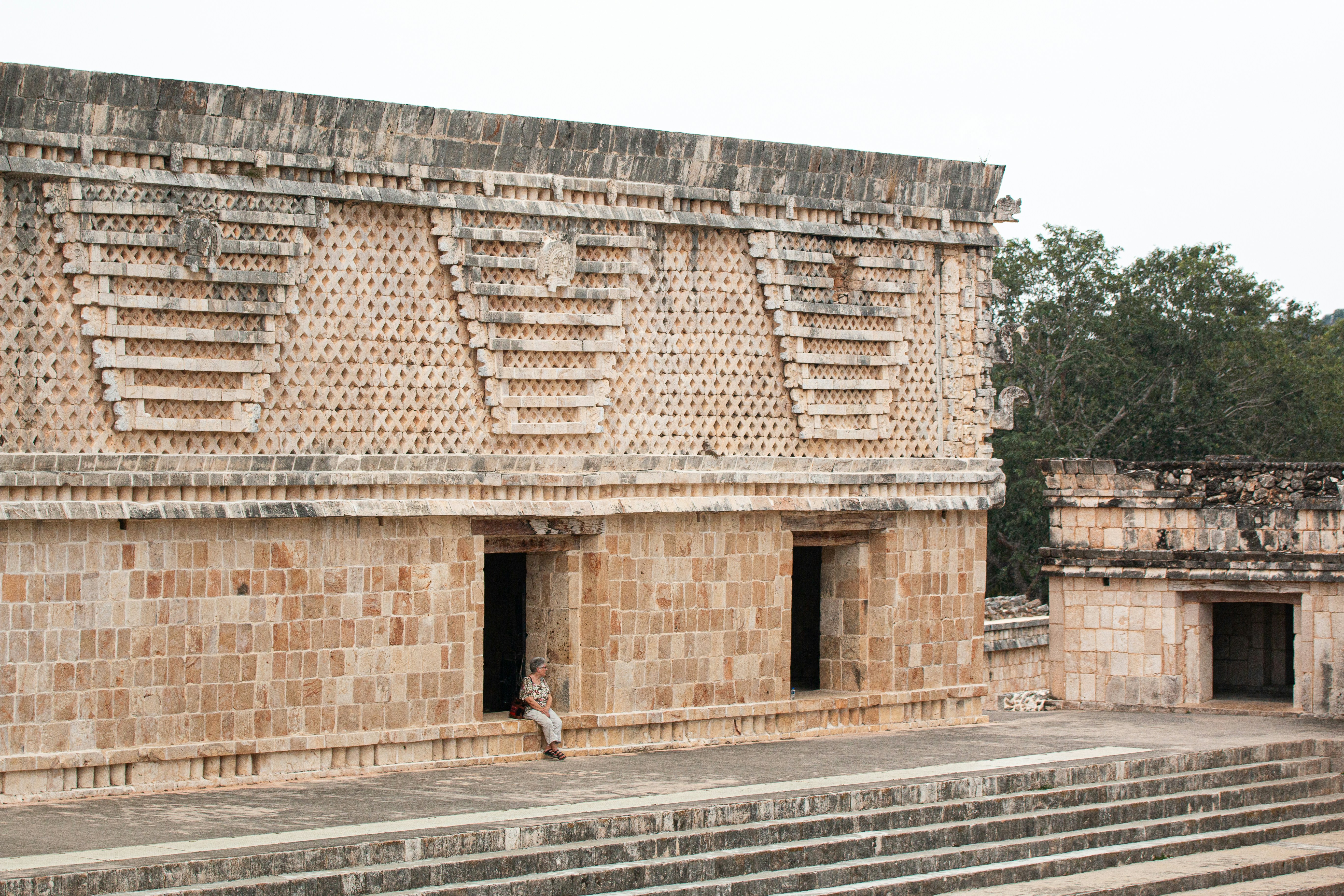 Intricate stone architecture of a historic building, showcasing unique patterns and textures, with a solitary figure seated nearby. 