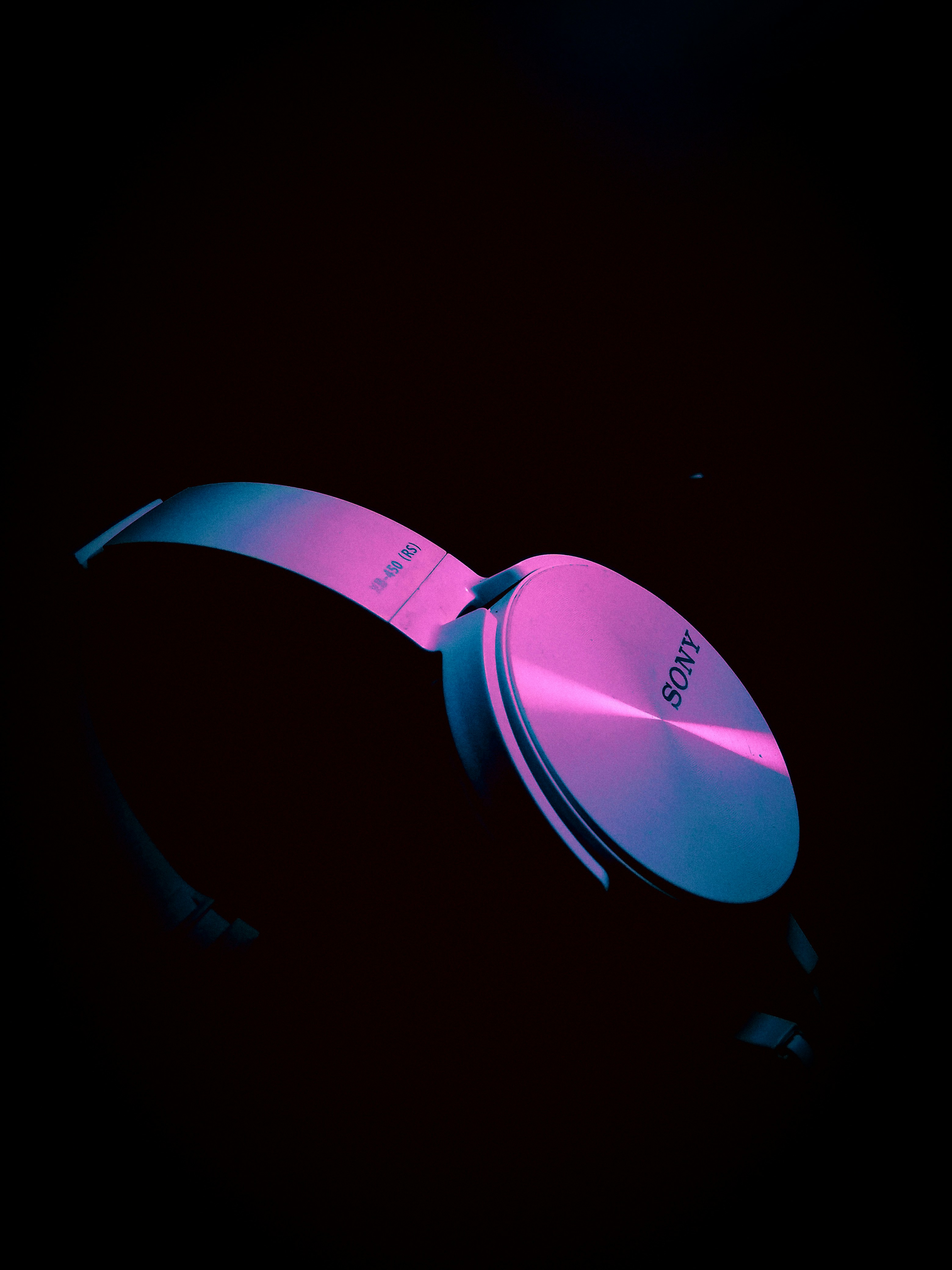 Pink neon-lit Sony headphones sit against a dark background, highlighting the glossy circular ear cup.