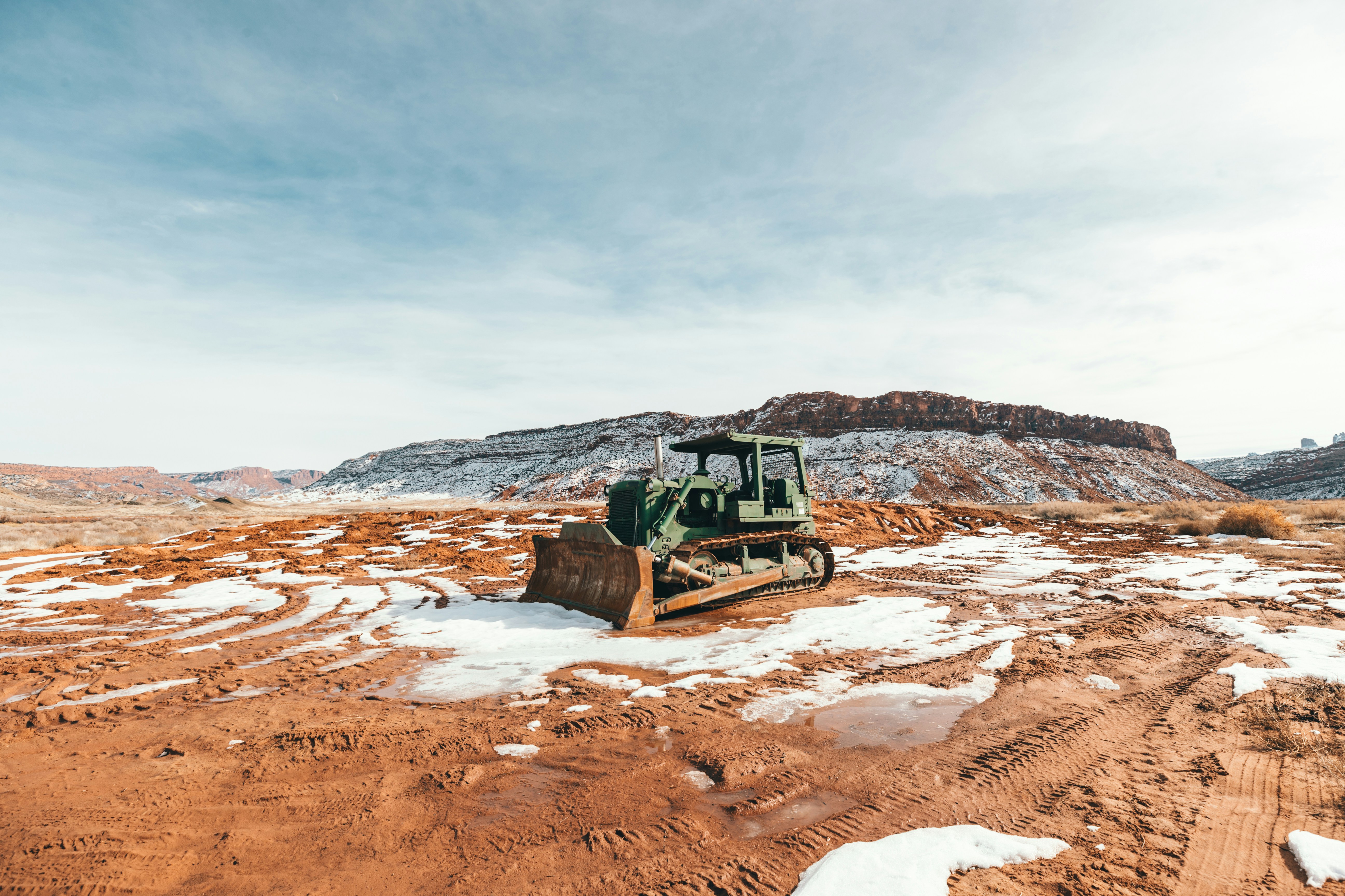 Green Bulldozer Amid Snow-Touched Red Terrain Under Expansive Sky
