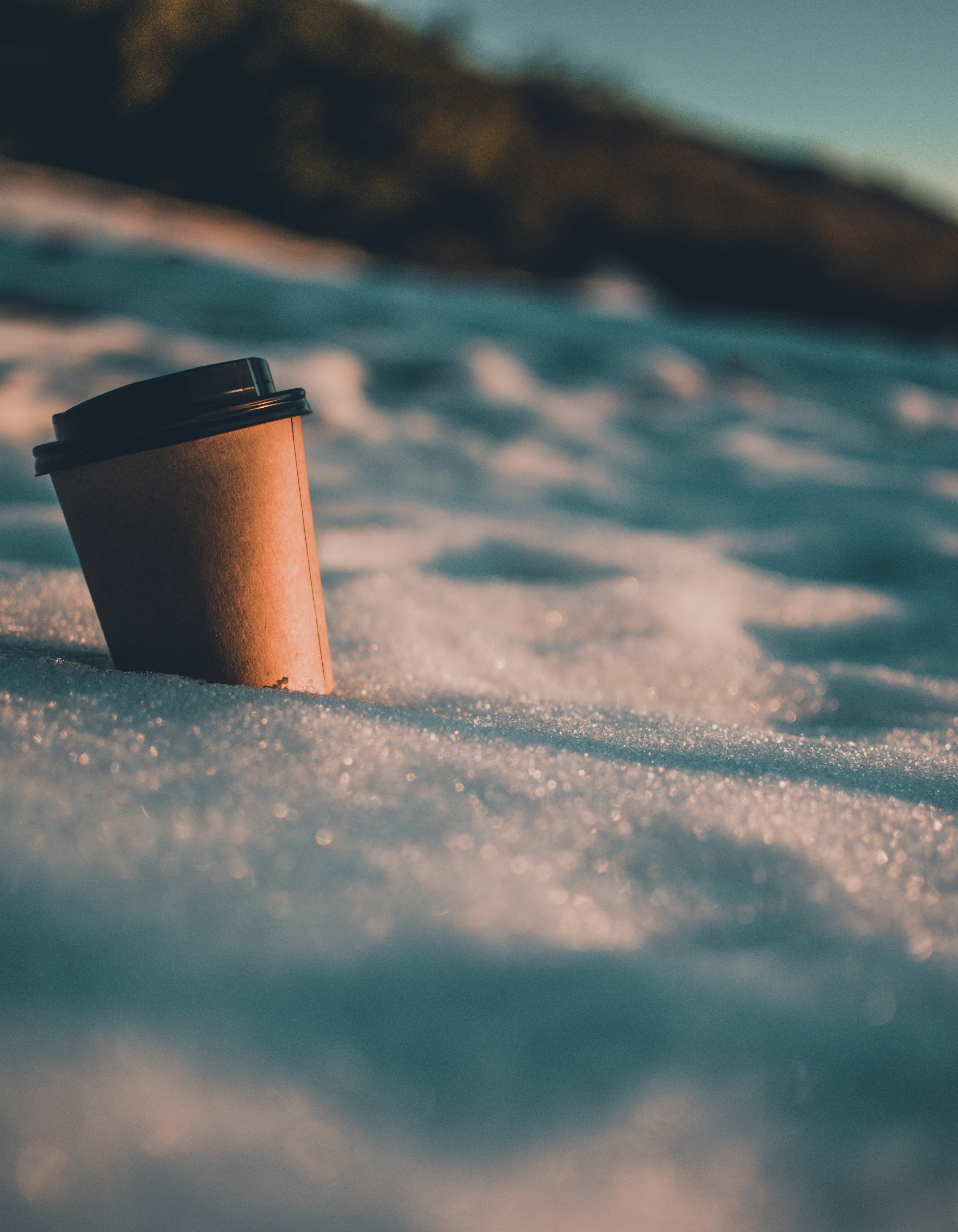 Disposable coffee cup resting on a blanket of snow, capturing the contrast between warmth and cold. The soft lighting enhances the serene winter atmosphere.