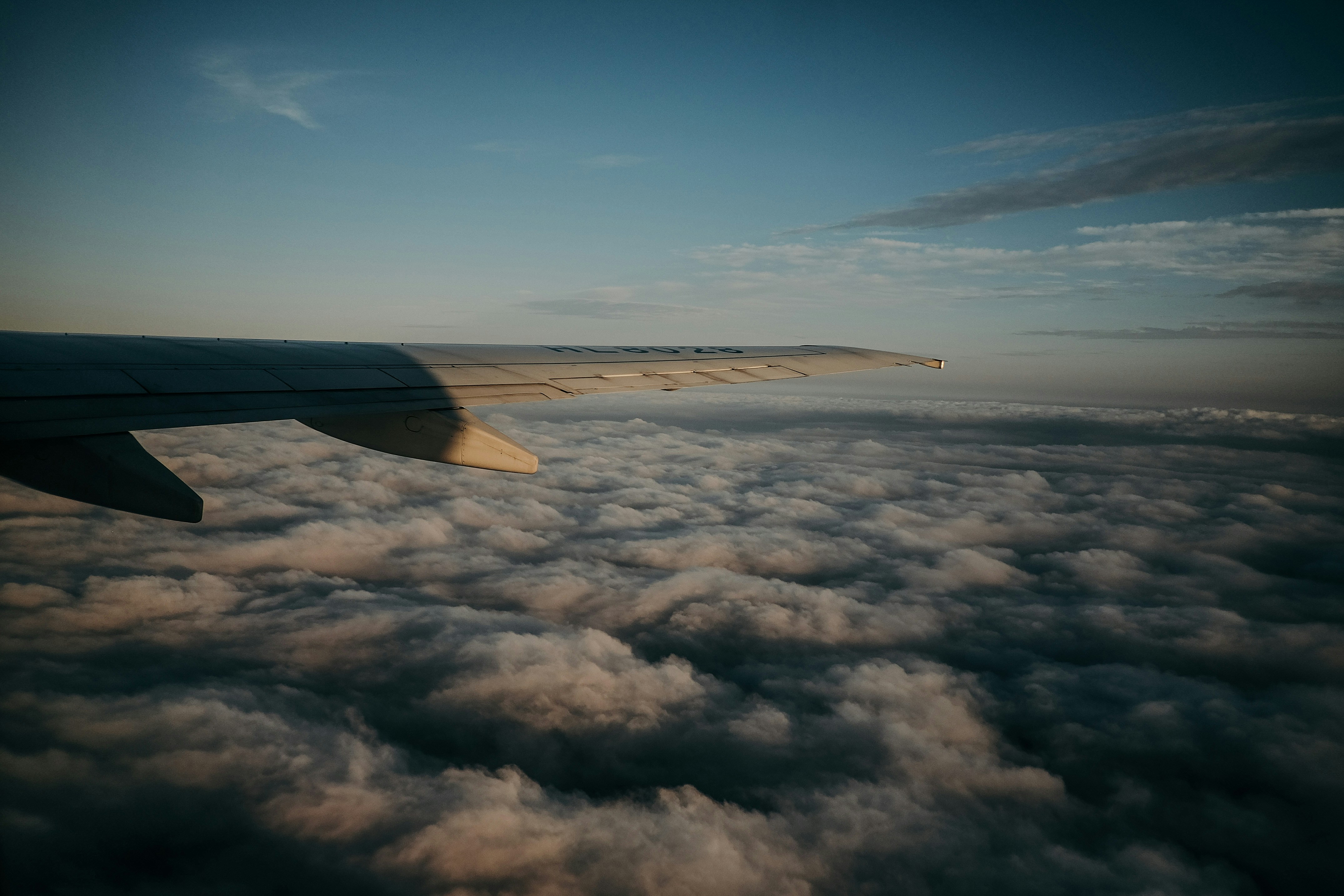 Airplane wing slicing through a sea of fluffy clouds during a serene flight. The soft light creates a tranquil atmosphere.