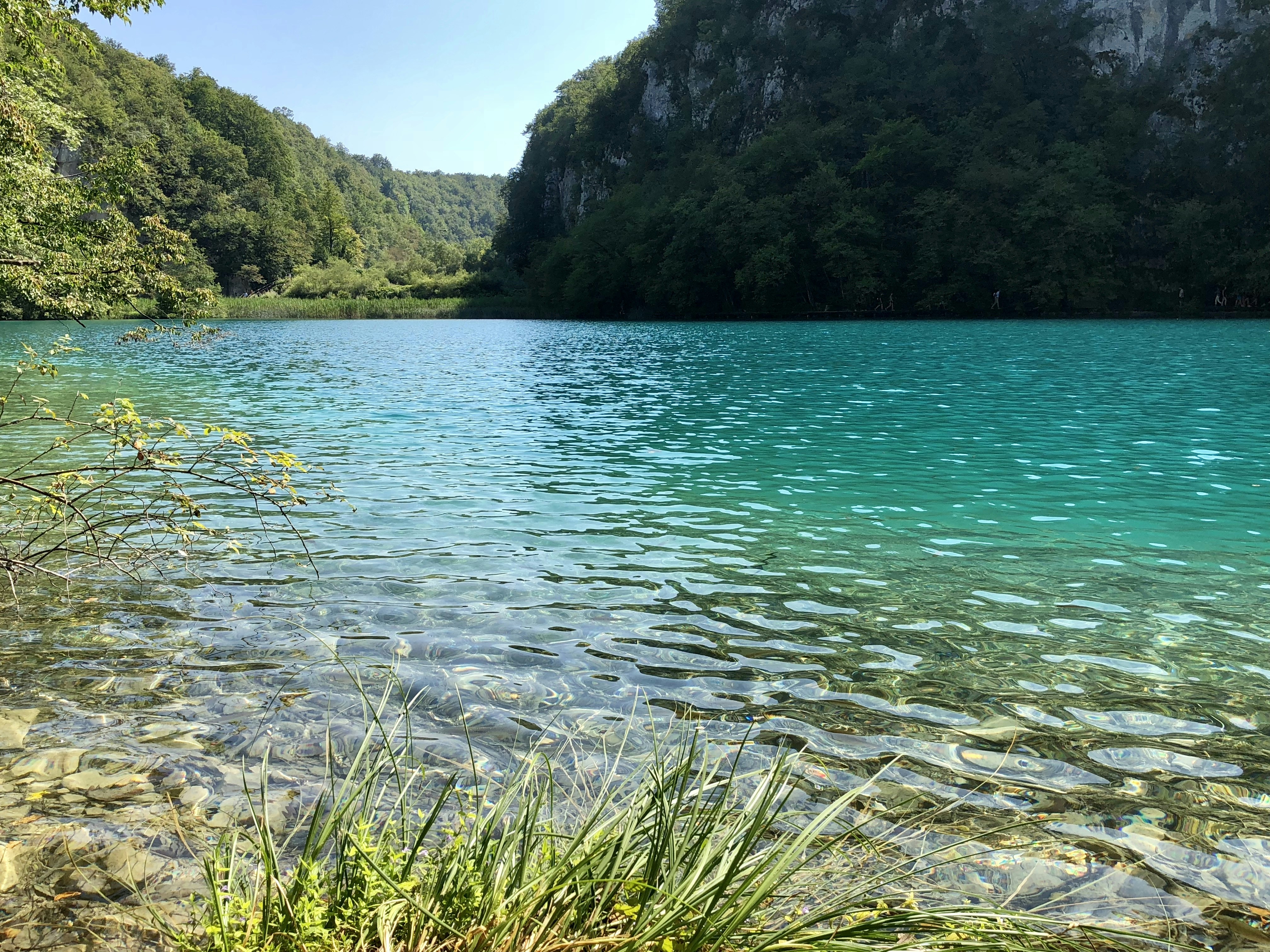 Clear turquoise lake surrounded by lush green hills under a bright blue sky.