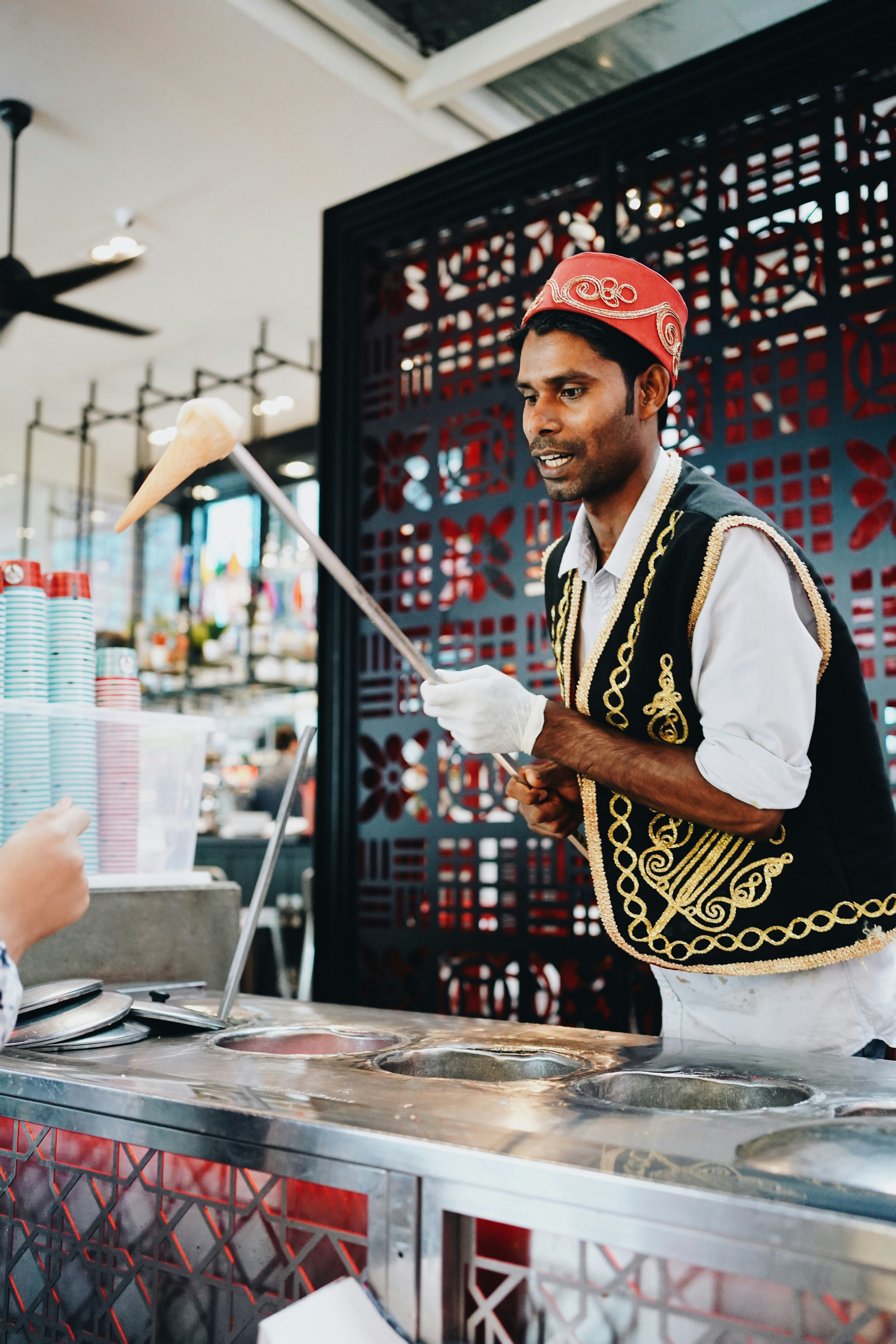 Man in traditional attire performing with an ice cream scoop at a lively market.