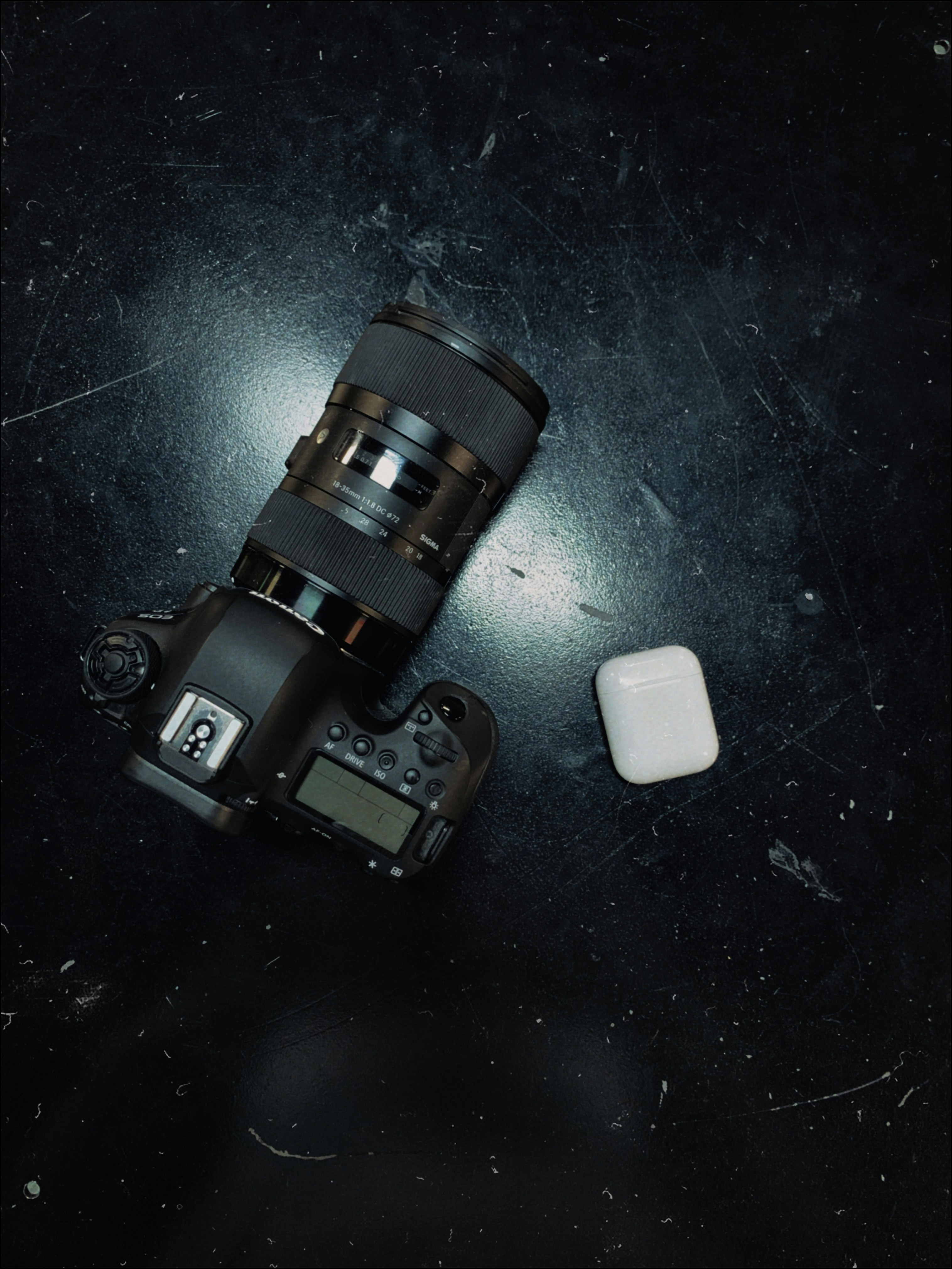 Midnight Gearscape: A DSLR with a Long Lens Beside a White AirPods Case
