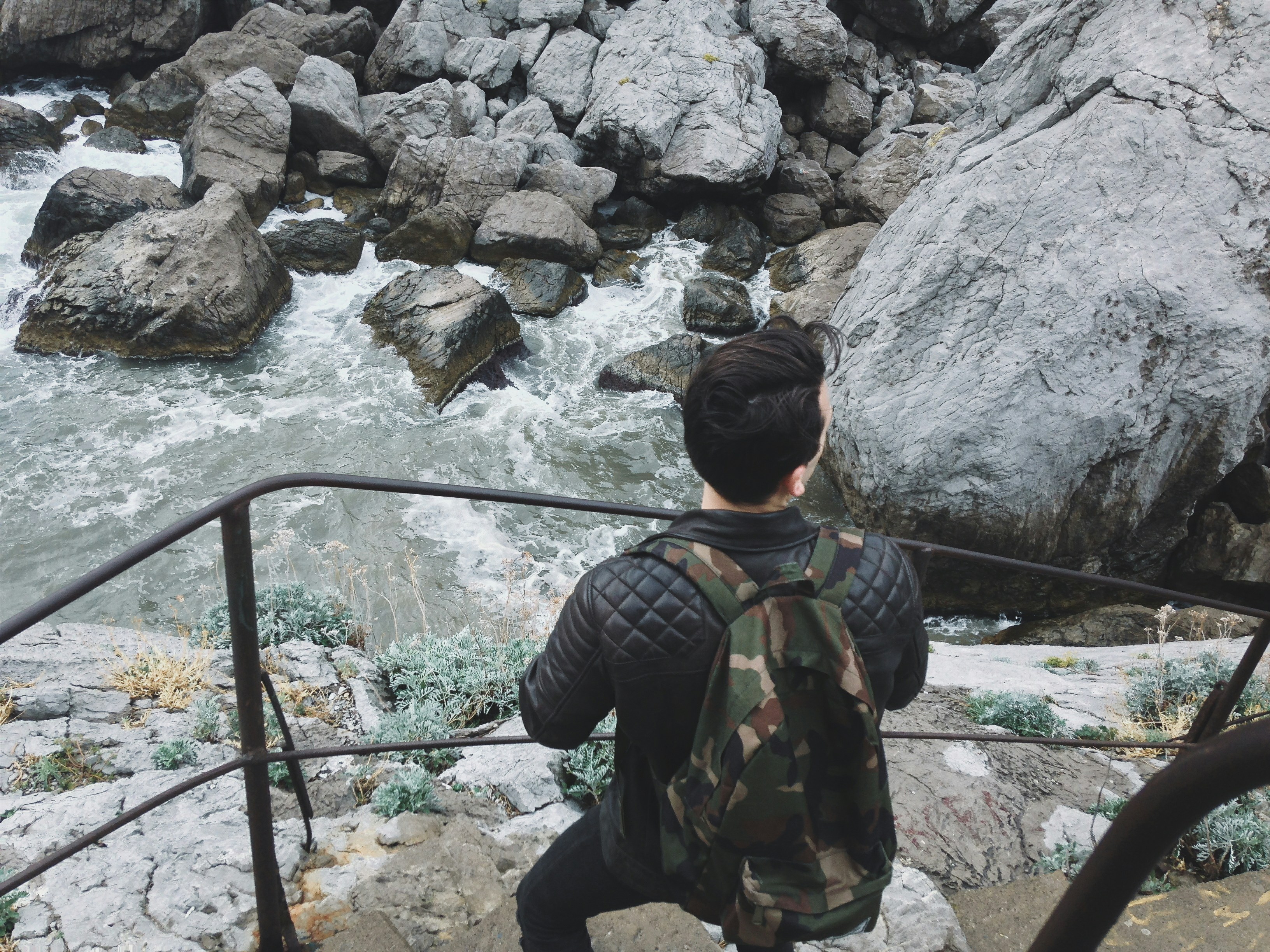 Rugged coastal overlook: a lone hiker surveys the surf from a rocky railing