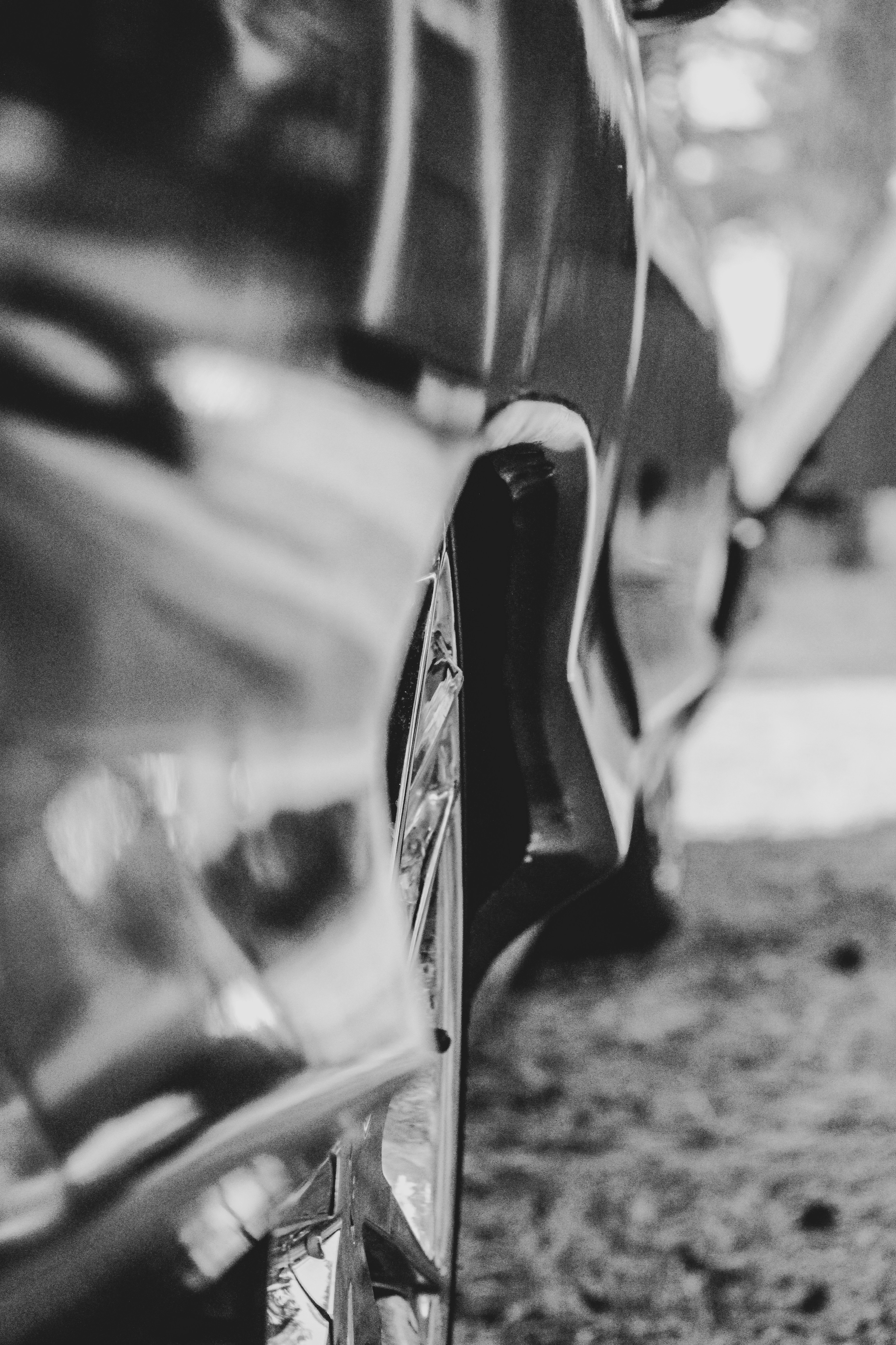 Close-up of a car wheel and body in black and white, showcasing reflections and textures.