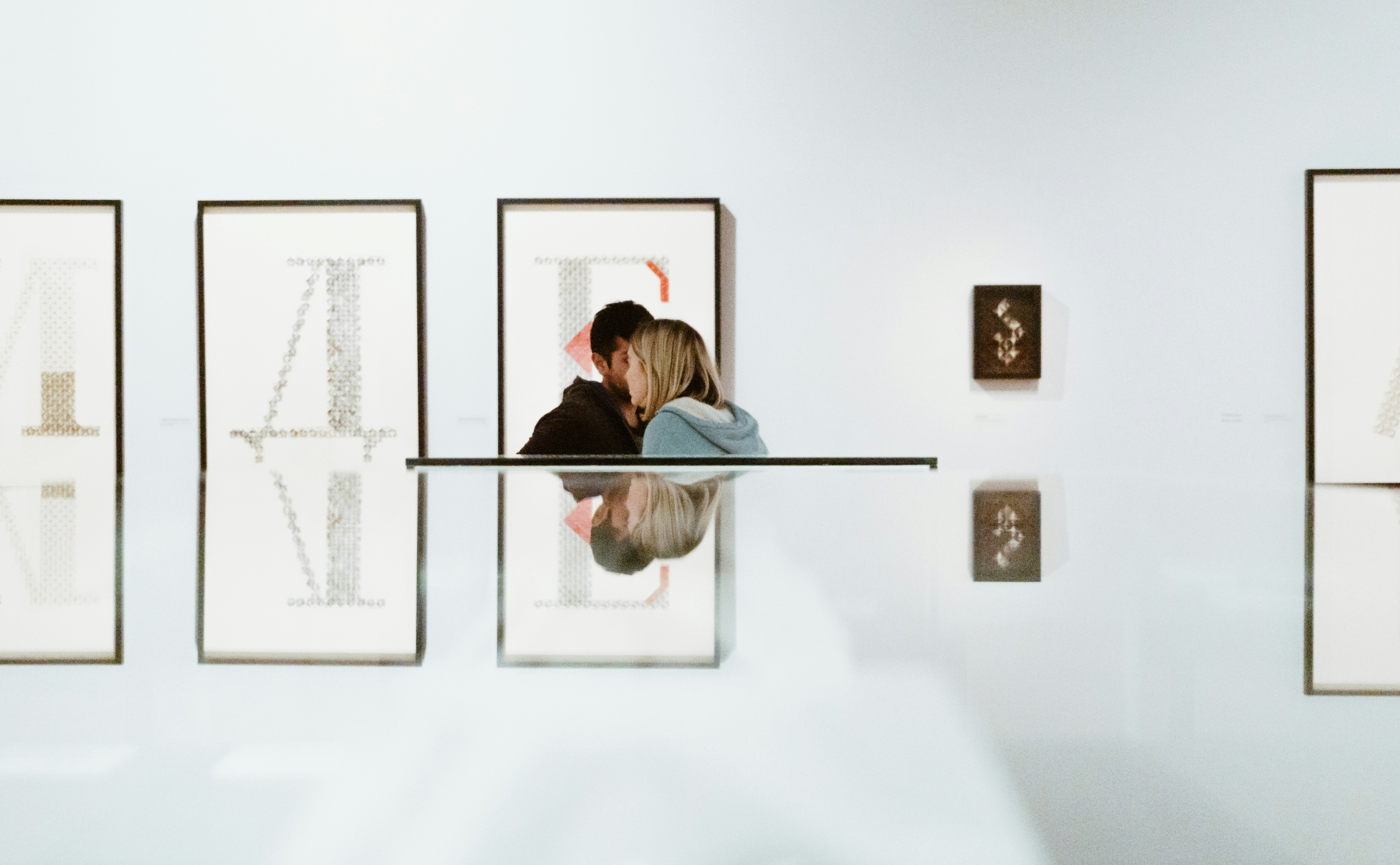 Couple standing closely in a modern art gallery surrounded by minimalist framed artworks on a white wall.