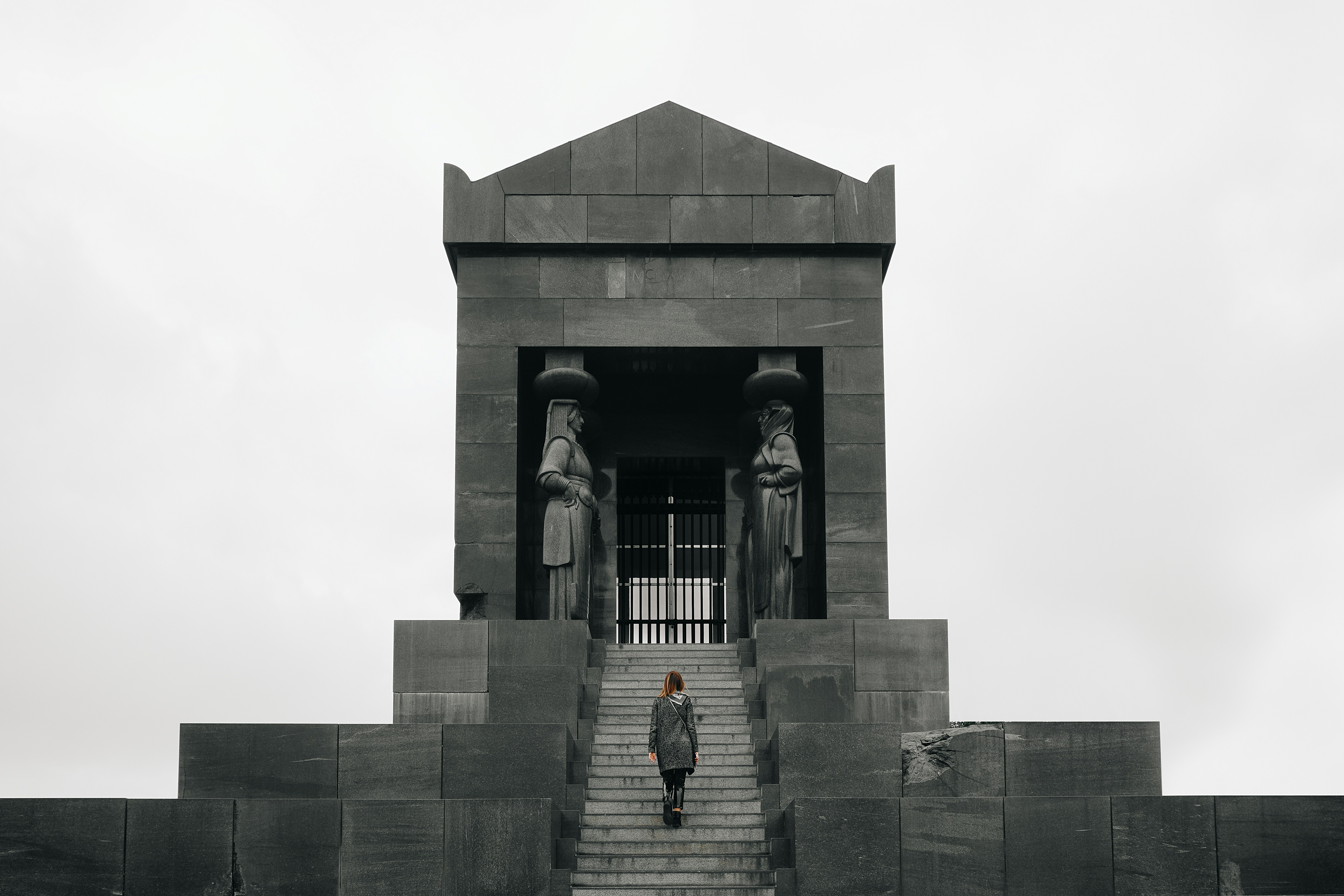 Person climbing steps toward a monumental stone structure under a cloudy sky.