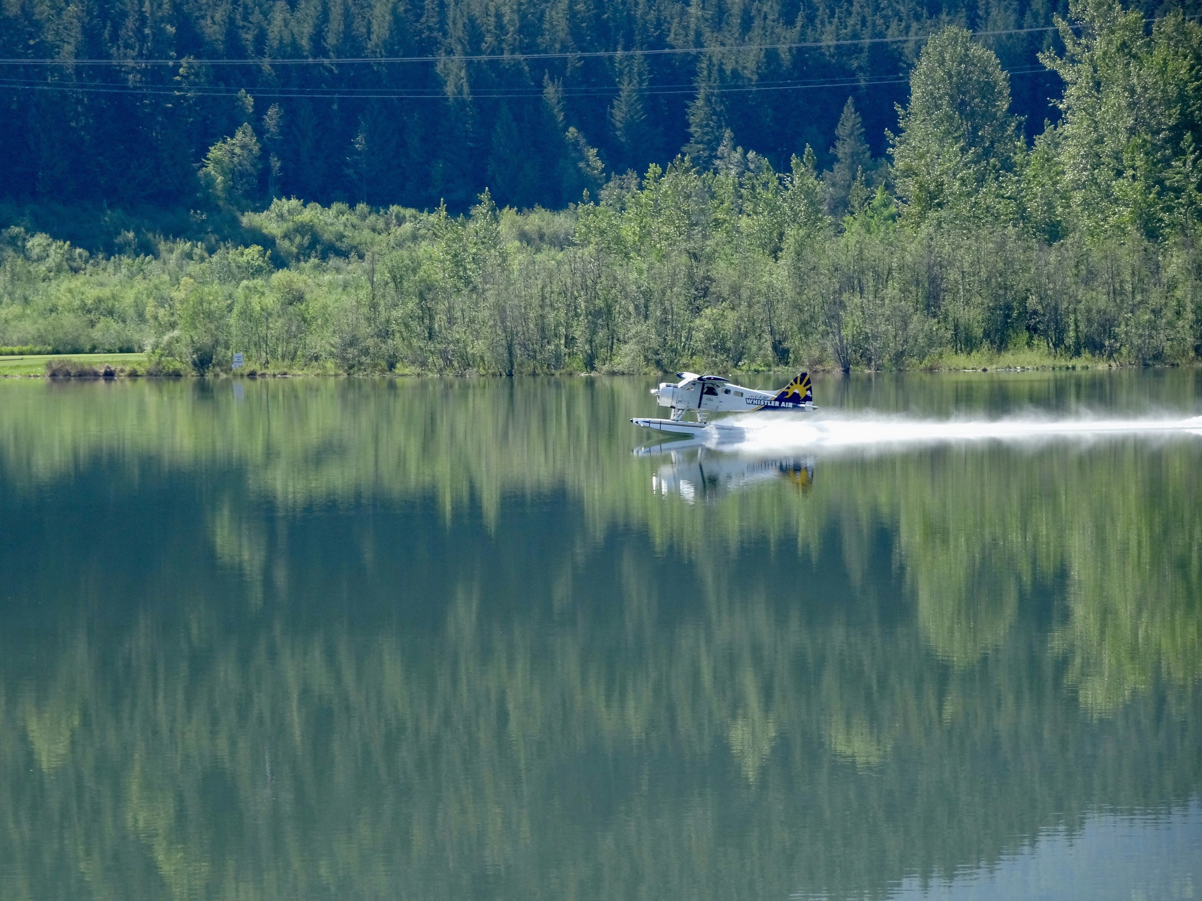 Seaplane skimming across Green Lake with forested hills reflecting in the water.