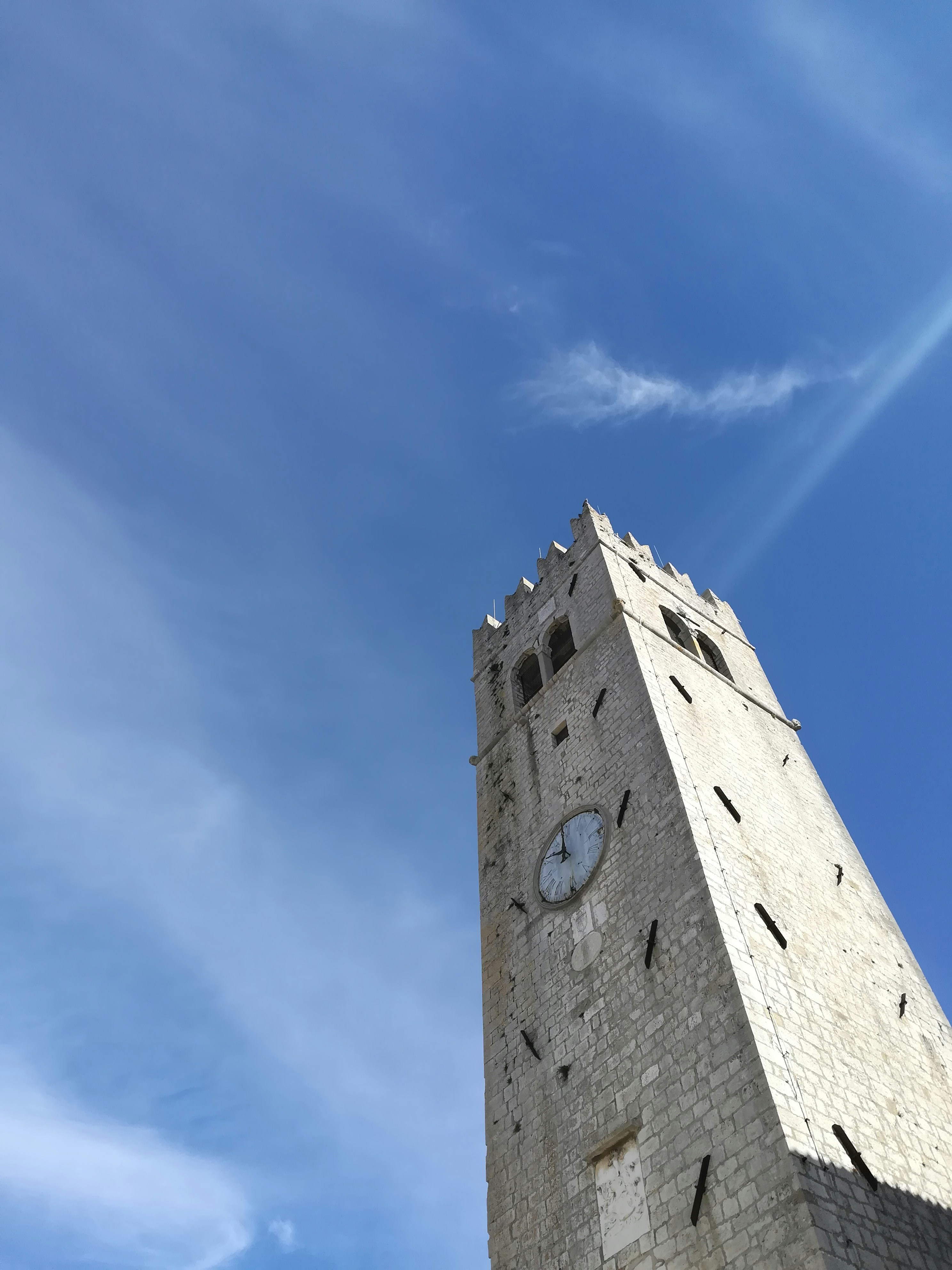 Historic clock tower reaching towards a vibrant blue sky, showcasing architectural details and a prominent clock face.