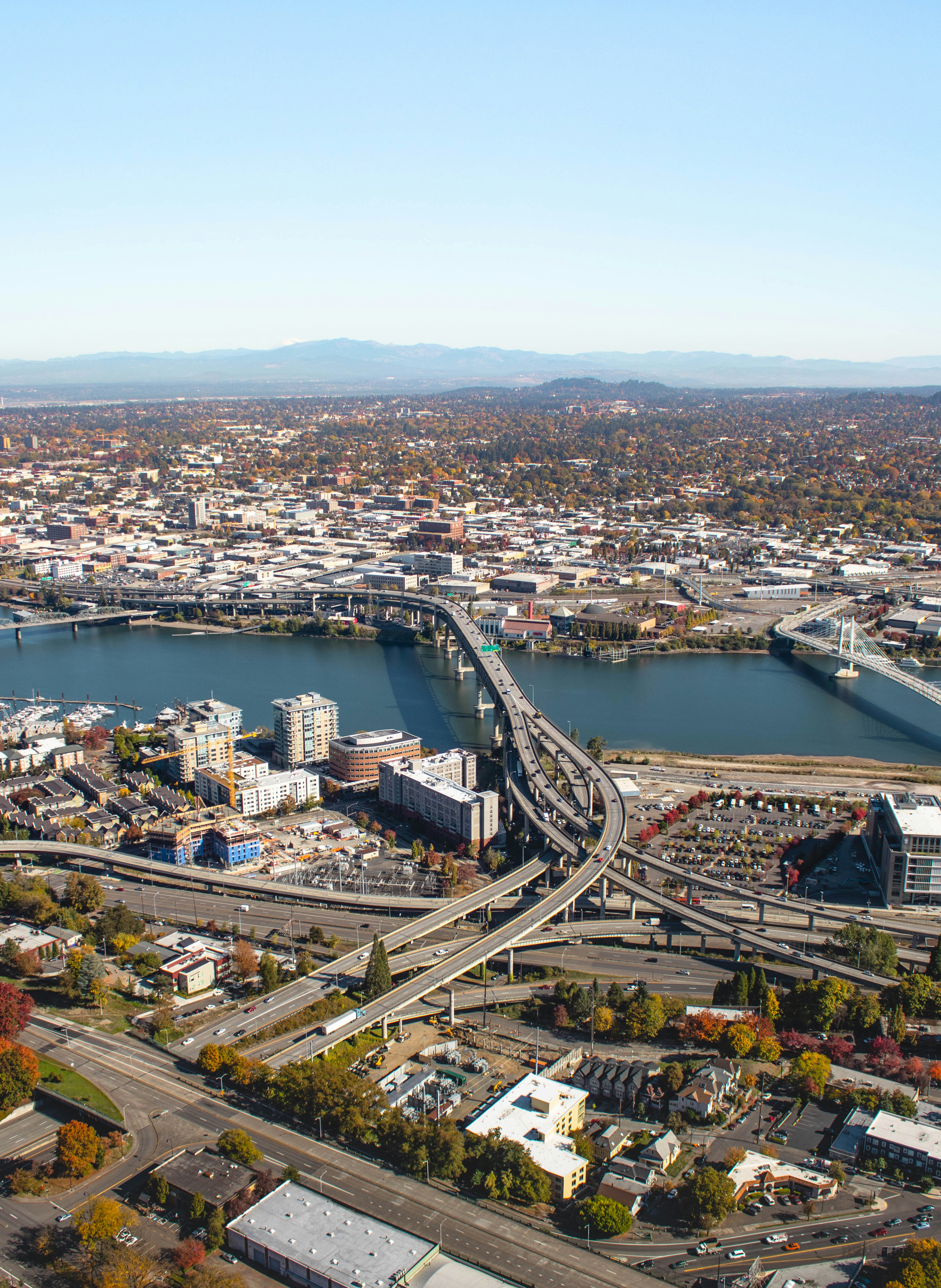 Aerial view showcasing a complex intersection of highways and waterways, framed by city buildings and autumn foliage.