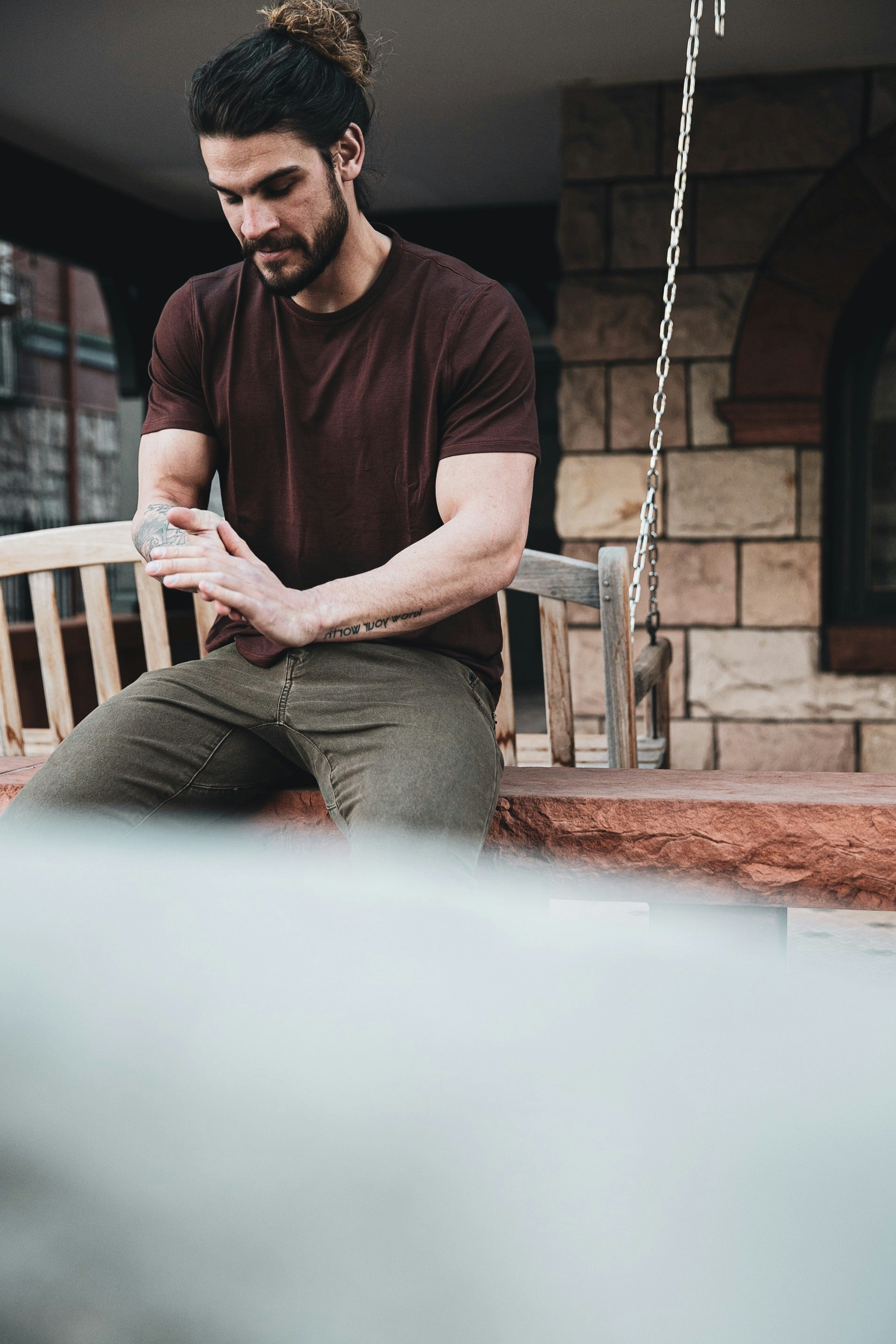 Man in maroon crew neck t-shirt and gray denim jeans sitting on brown ...
