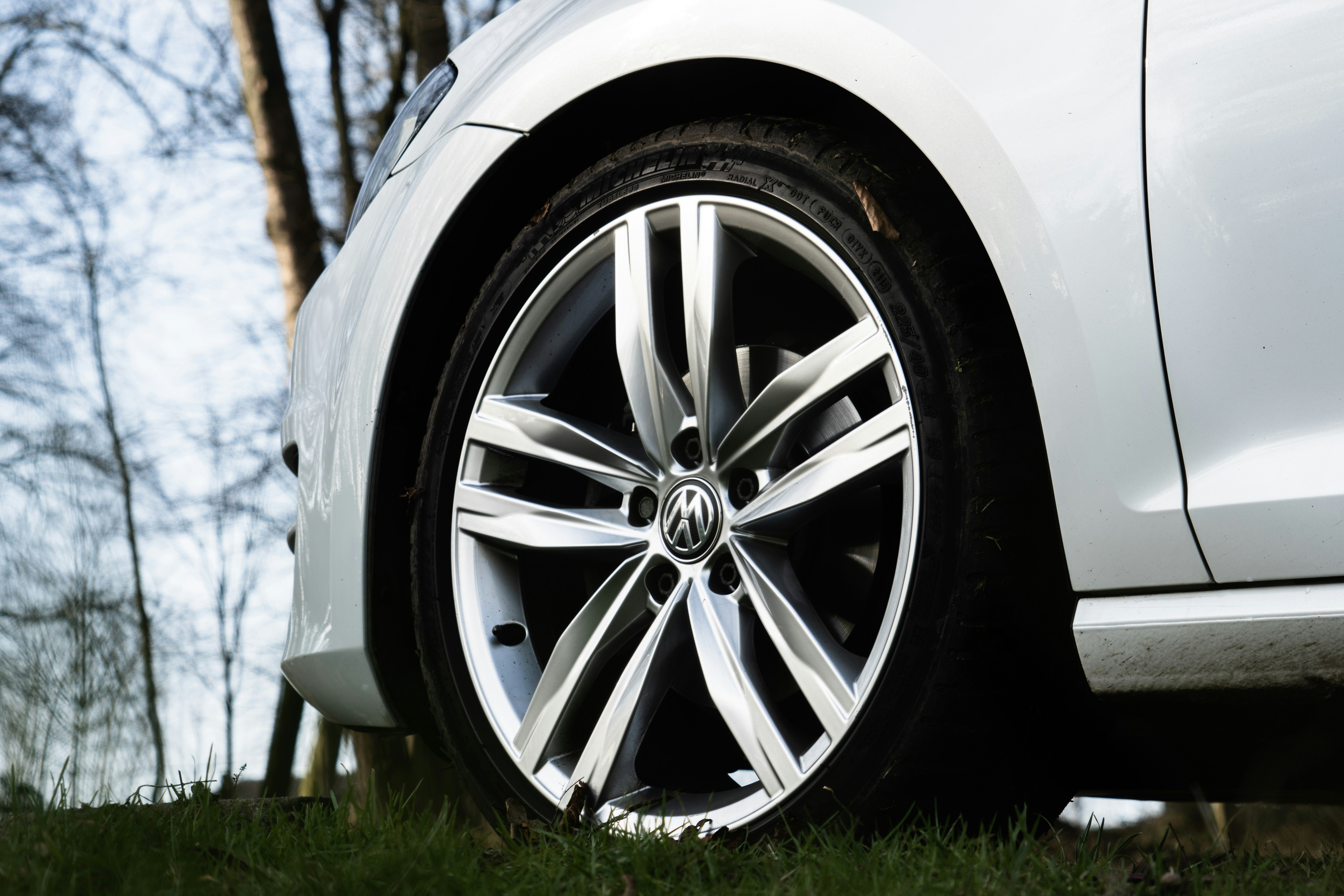 Silver VW wheel gleaming under a sunlit roadside scene