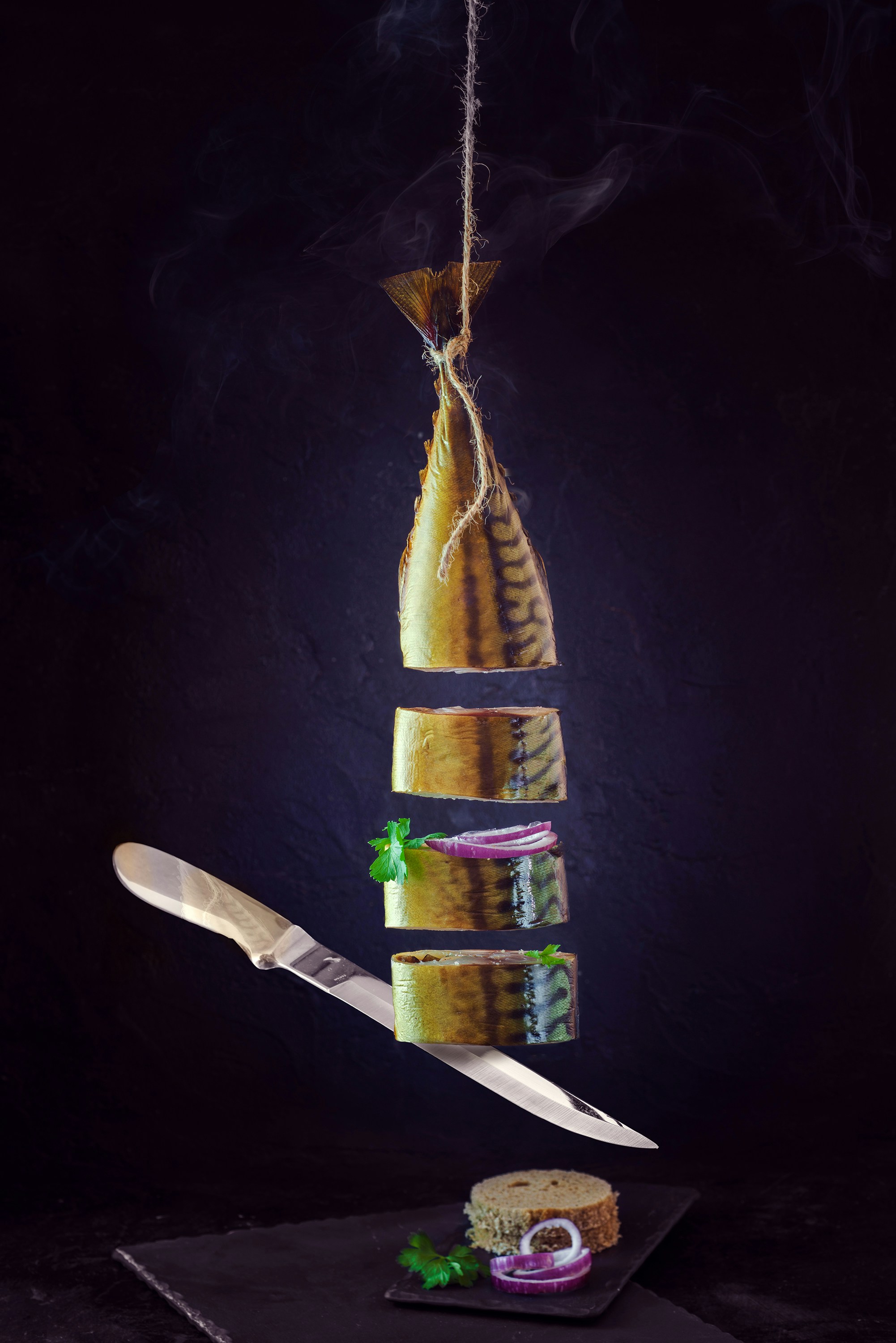 A beautifully arranged composition featuring a suspended fish, sliced vegetables, and a knife, set against a dark background. The scene highlights the art of culinary presentation.