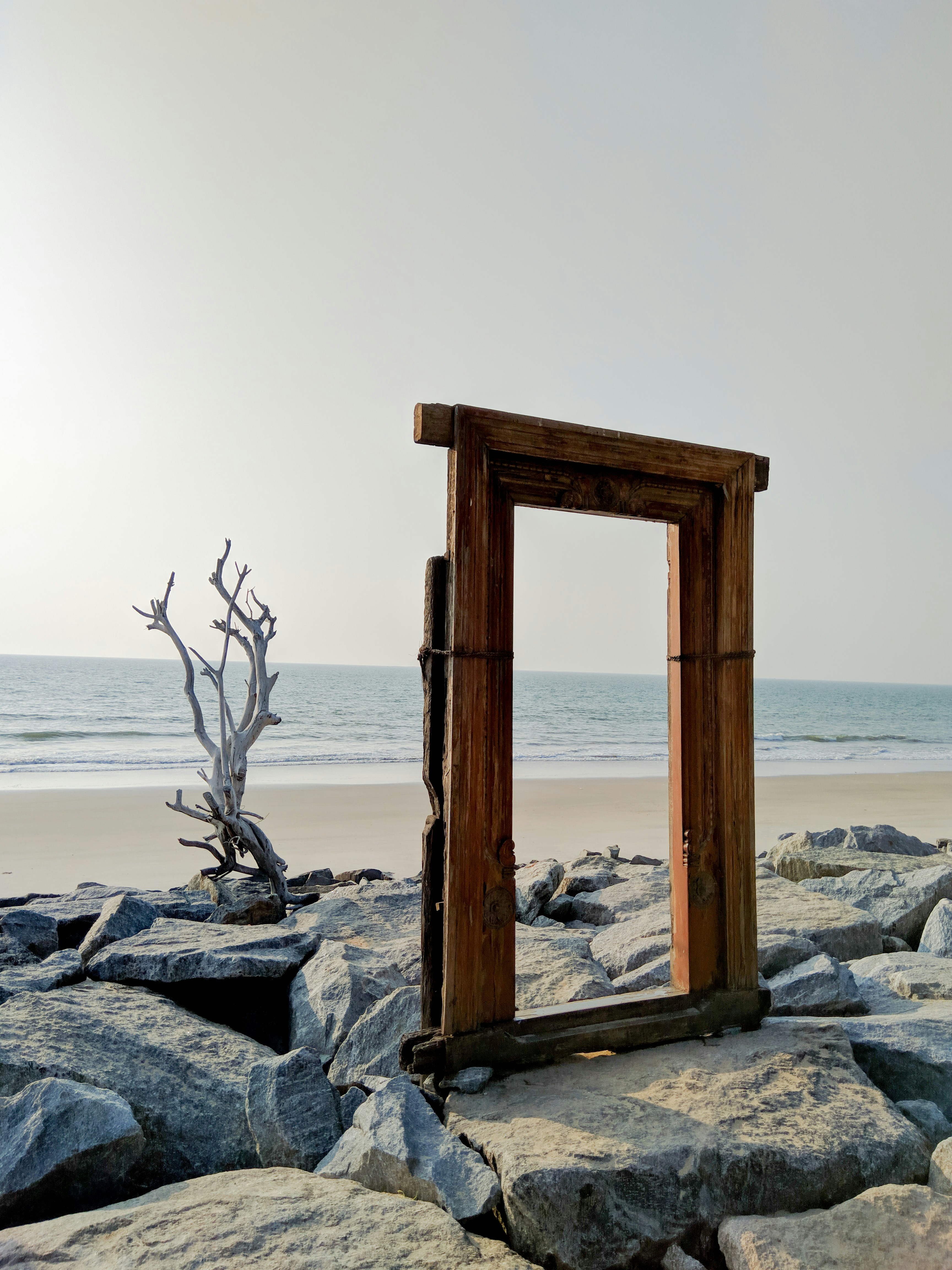 Doorway on the Shore: A Weathered Timber Frame Among Coastal Rocks