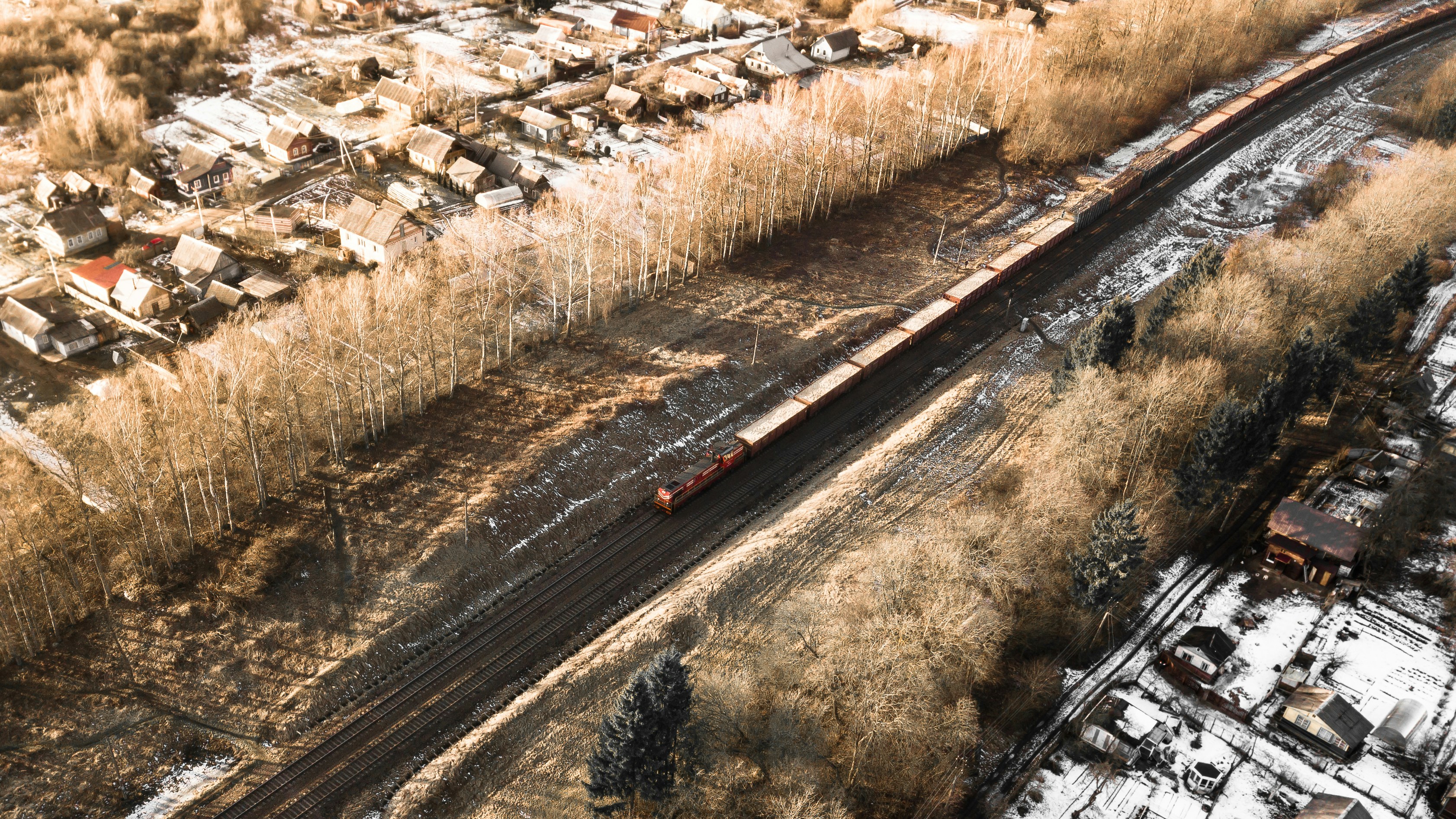 A train snakes through a winter landscape, flanked by bare trees and scattered homes, capturing the essence of rural tranquility.
