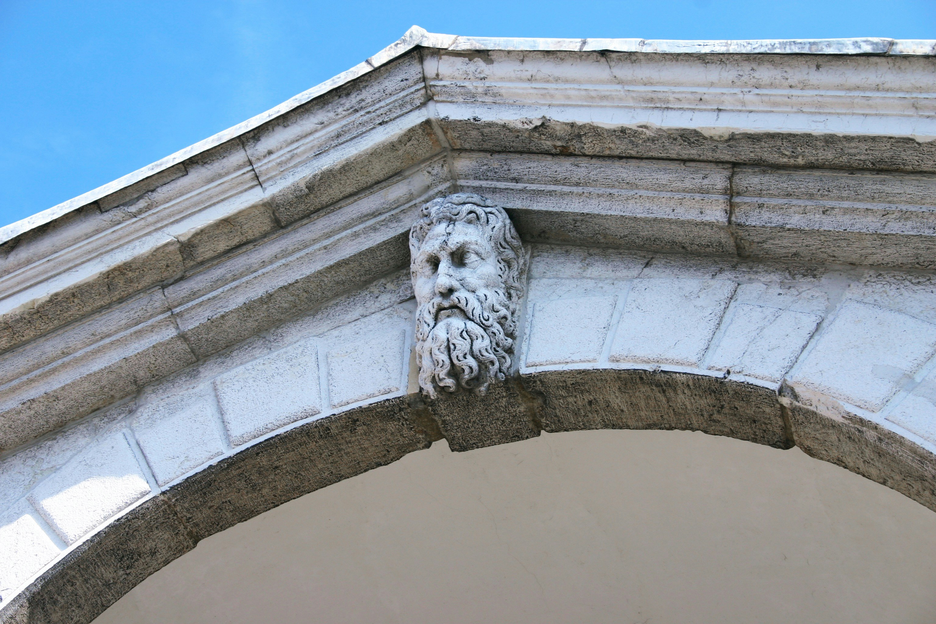 Intricate stone carving of a bearded figure adorning the edge of a classic archway, showcasing fine details and craftsmanship.