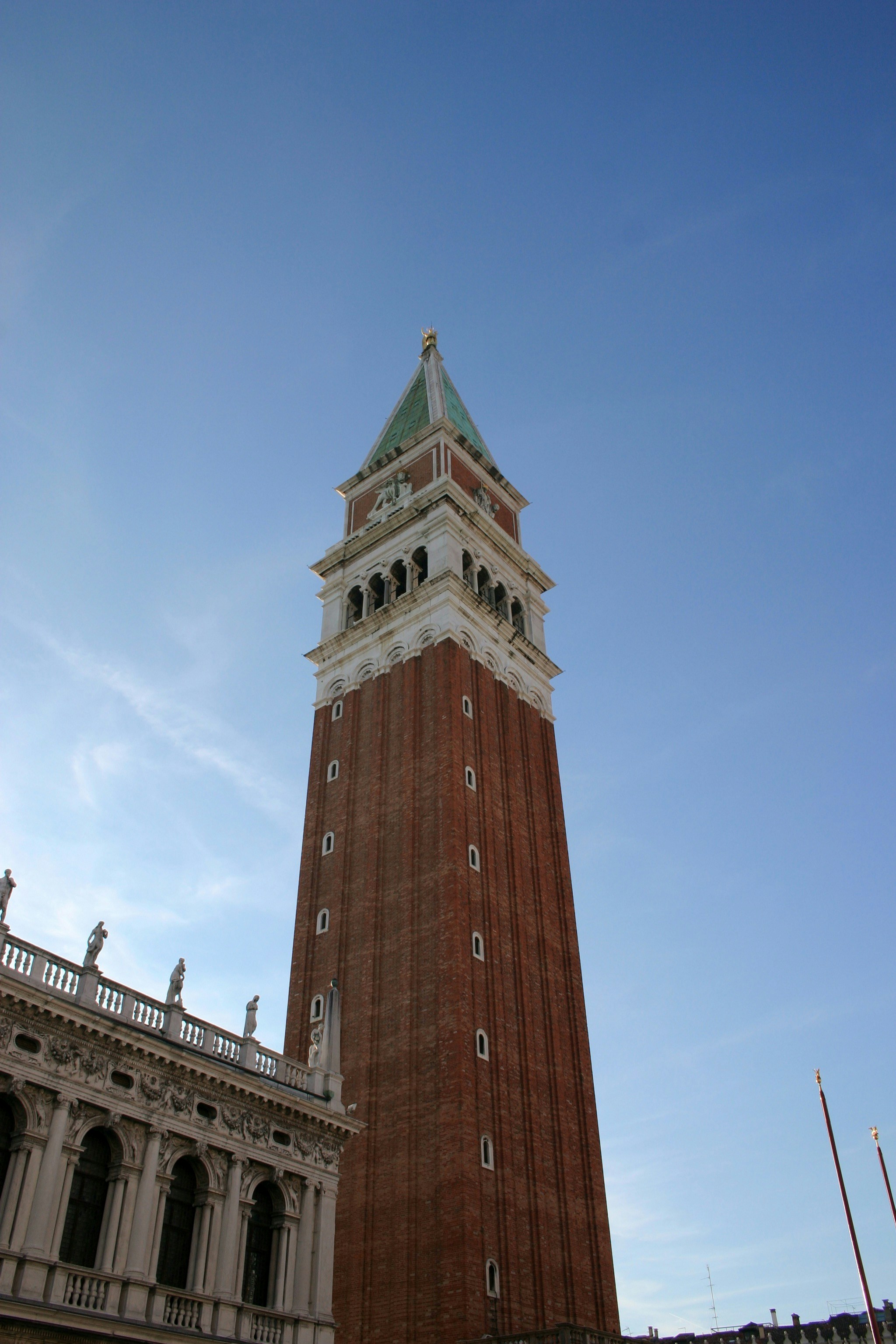Tall brick bell tower of St. Mark's Basilica in Venice, showcasing intricate architectural details against a clear blue sky.