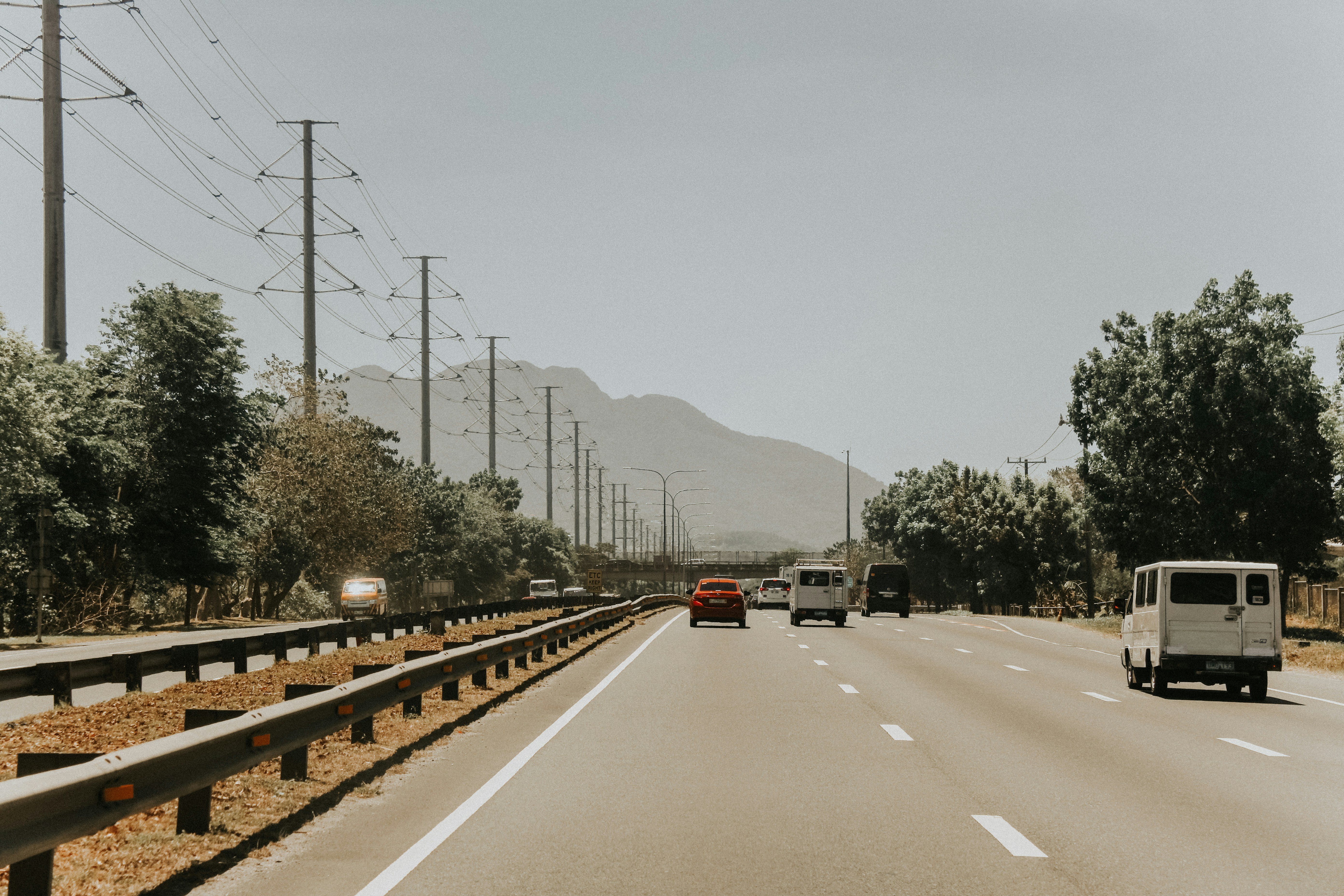 A serene highway scene with vehicles traveling amidst lush greenery and distant mountains, capturing the essence of a peaceful road trip.