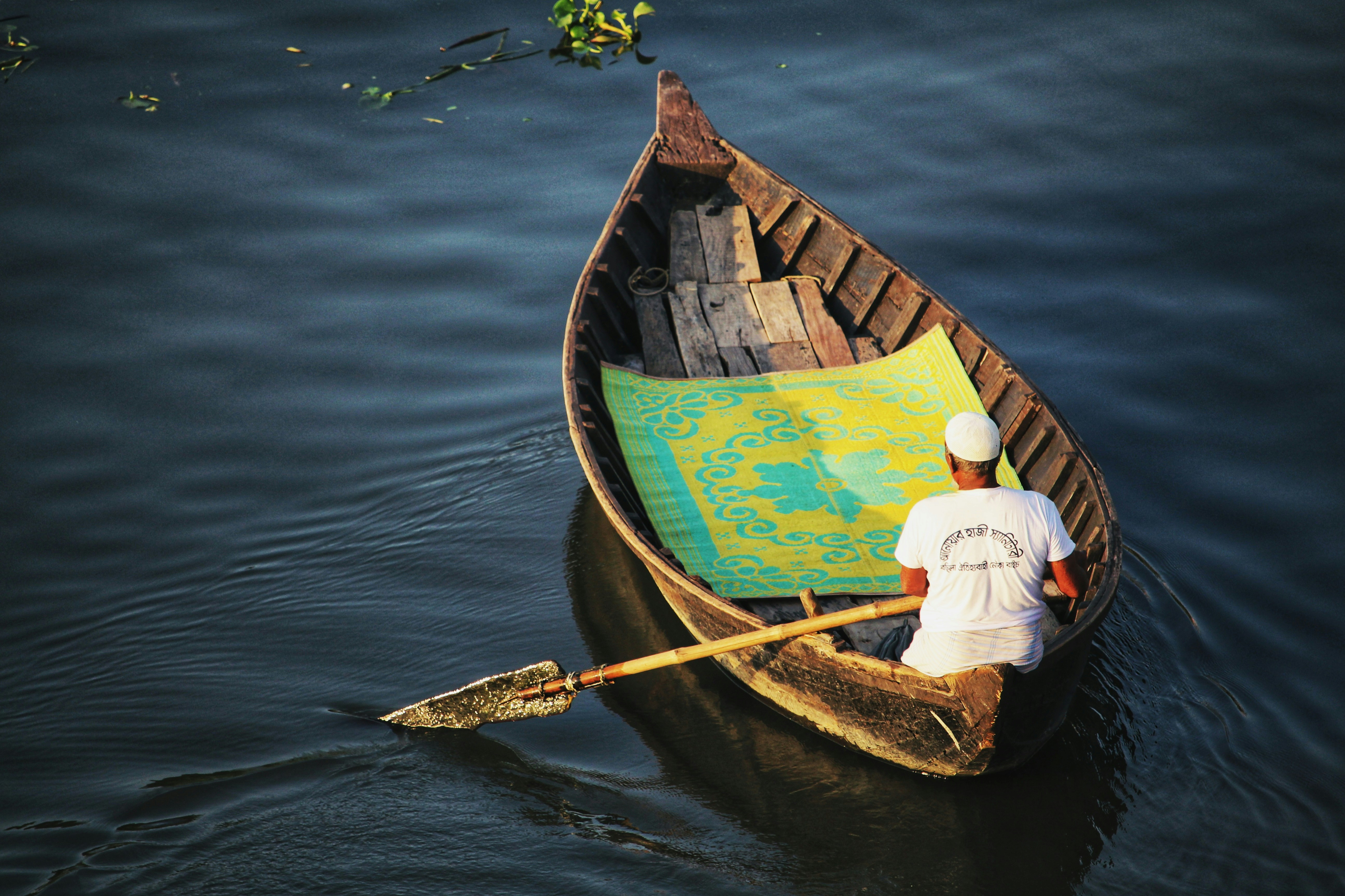 Wooden boat with a single rower navigating calm waters under a warm light.