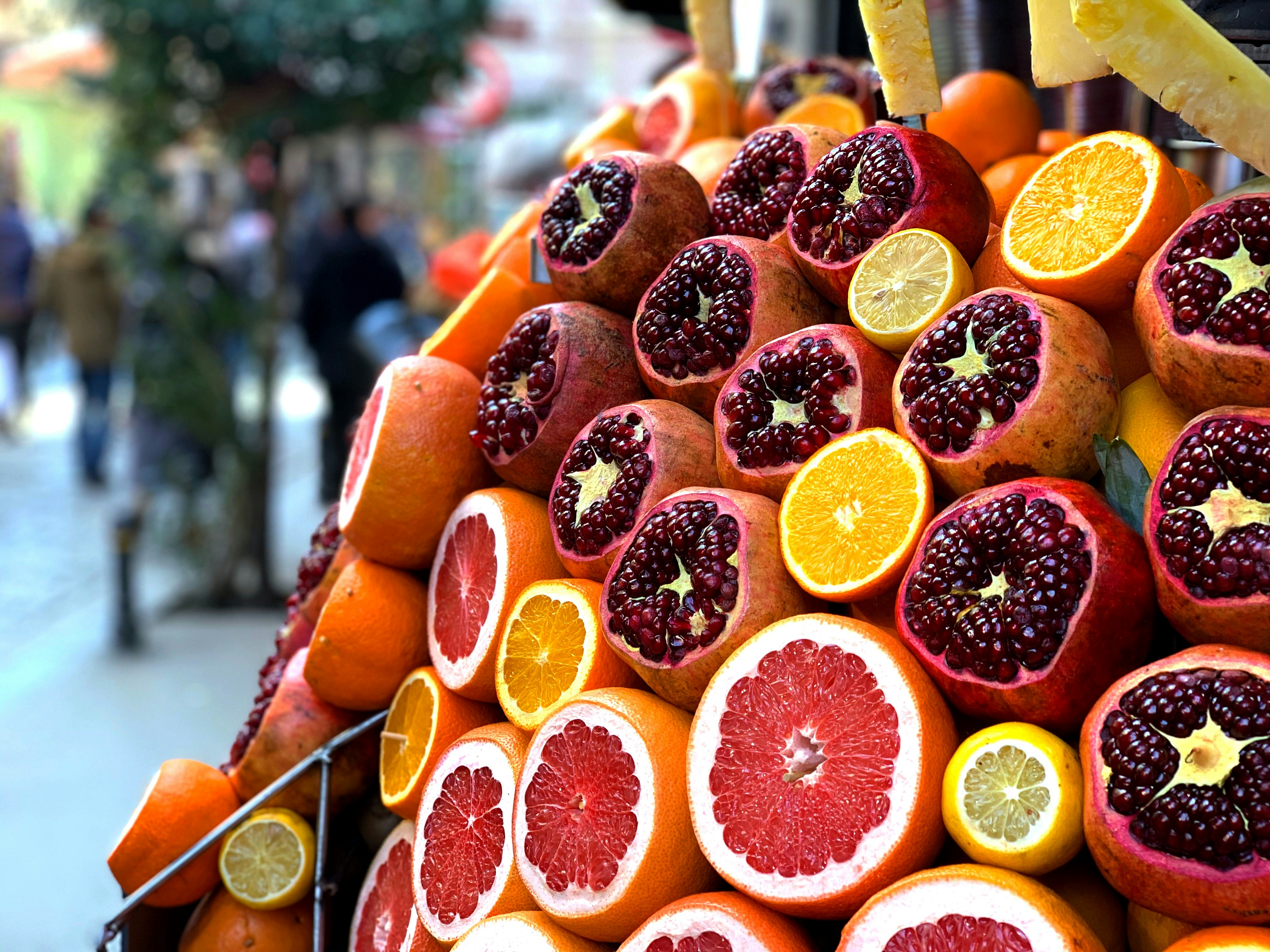 Vibrant arrangement of pomegranates, grapefruits, and oranges stacked in a market display. The colorful fruits invite passersby to indulge in their fresh offerings.