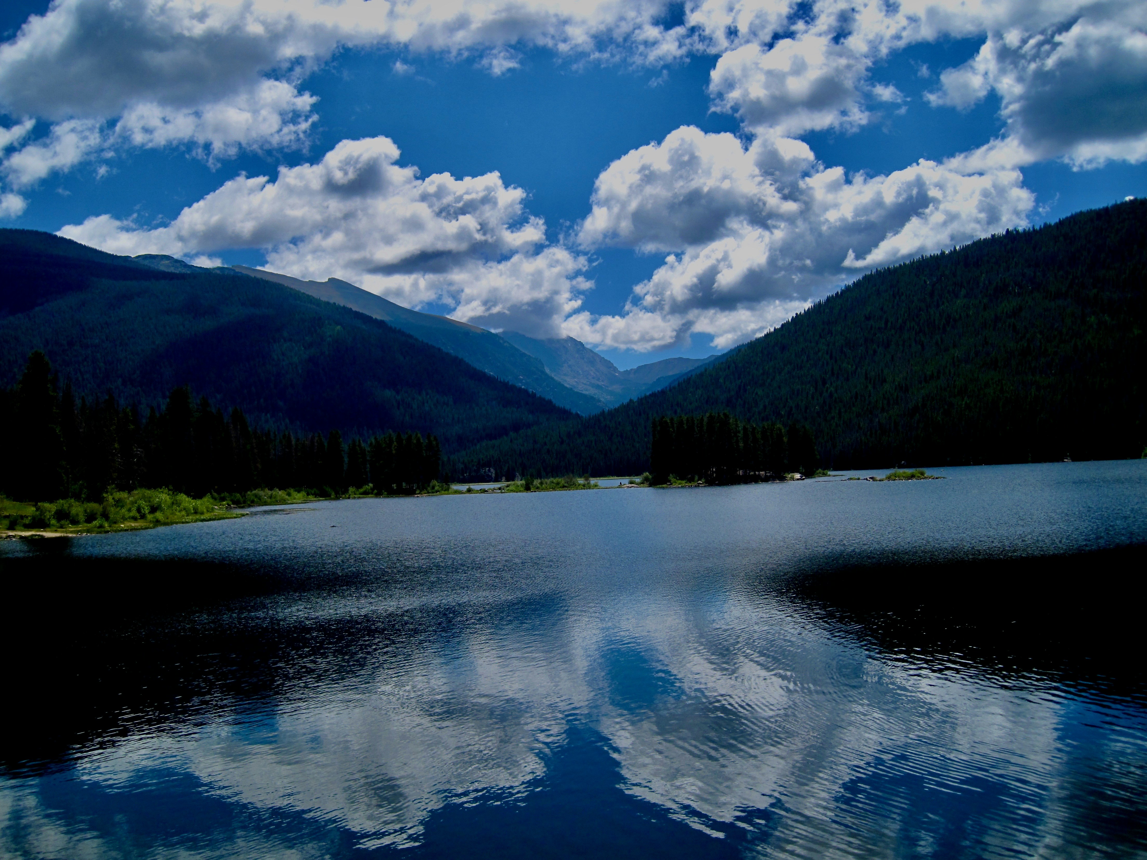 Serene lake reflecting majestic mountains and dynamic clouds under a vibrant sky.