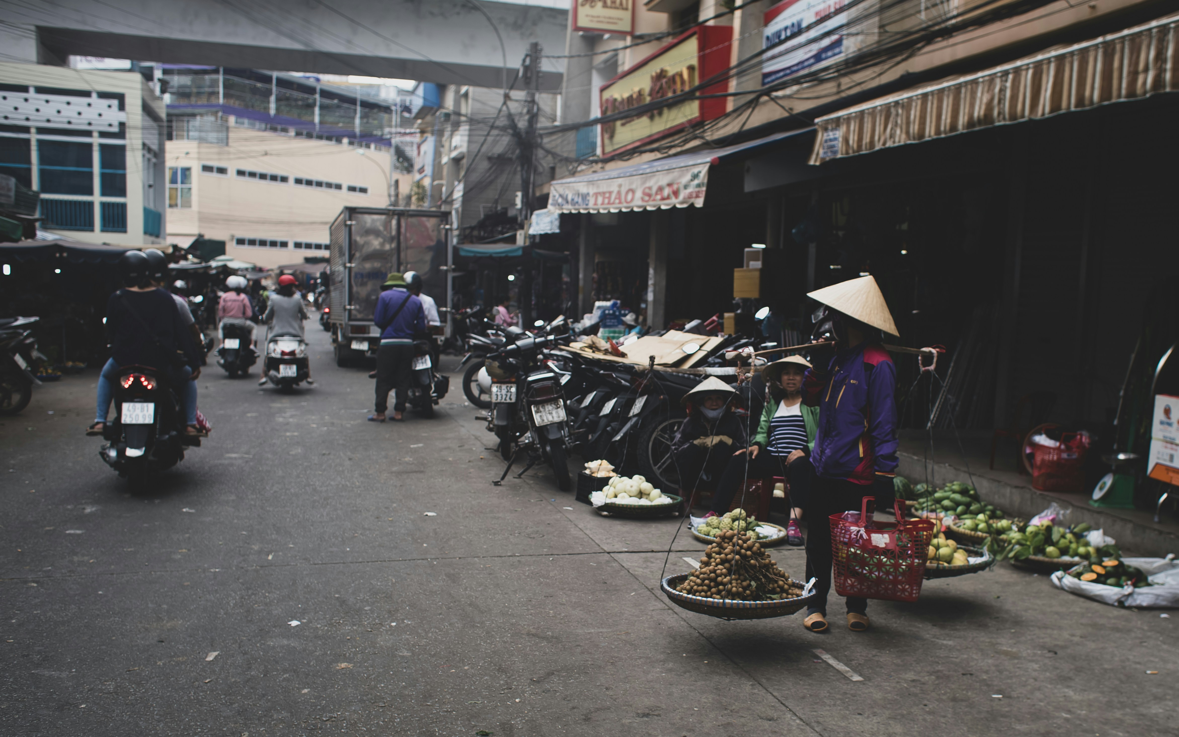 A bustling street market scene featuring vendors and motorcycles, showcasing local commerce and culture. The atmosphere is lively with various goods displayed for sale.