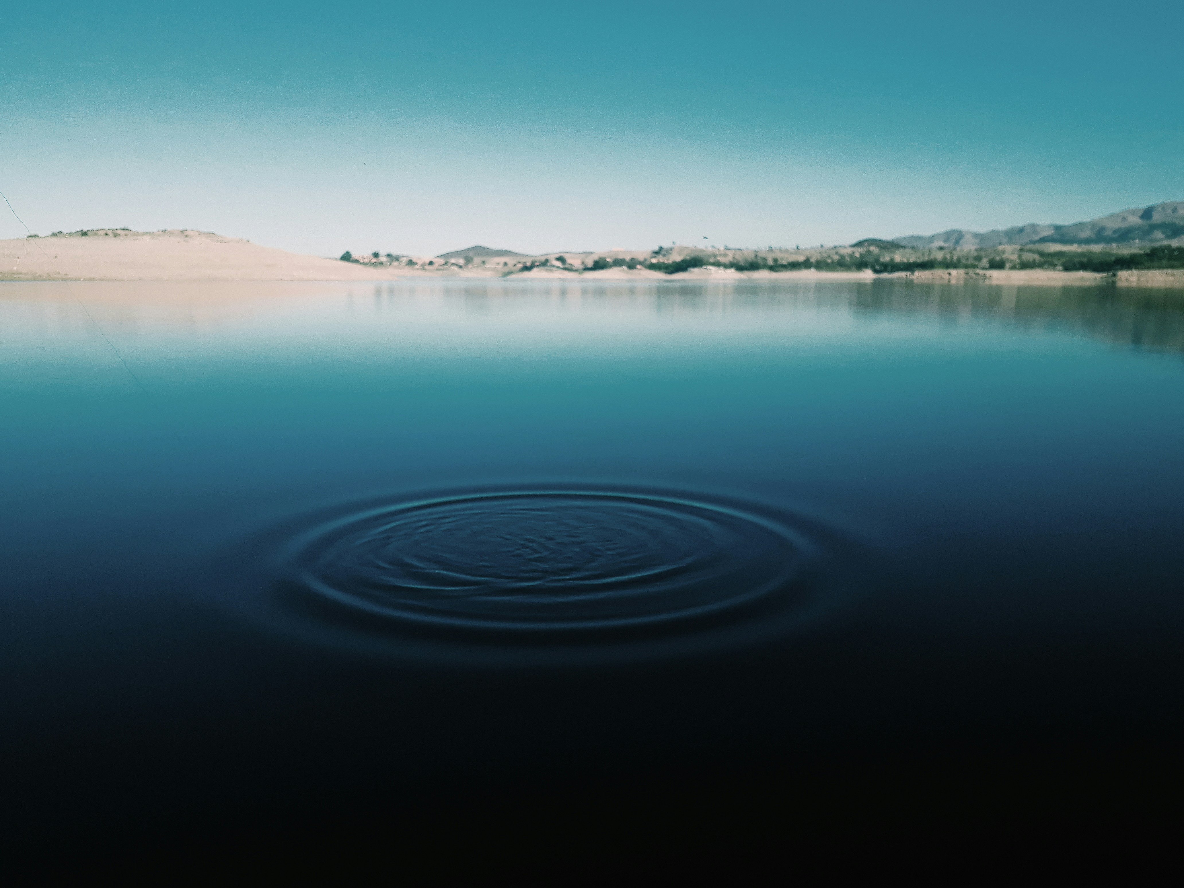 A tranquil lake reflecting the clear sky, disrupted only by the gentle ripples emanating from a single drop. The scene evokes a sense of calm and connection with nature.