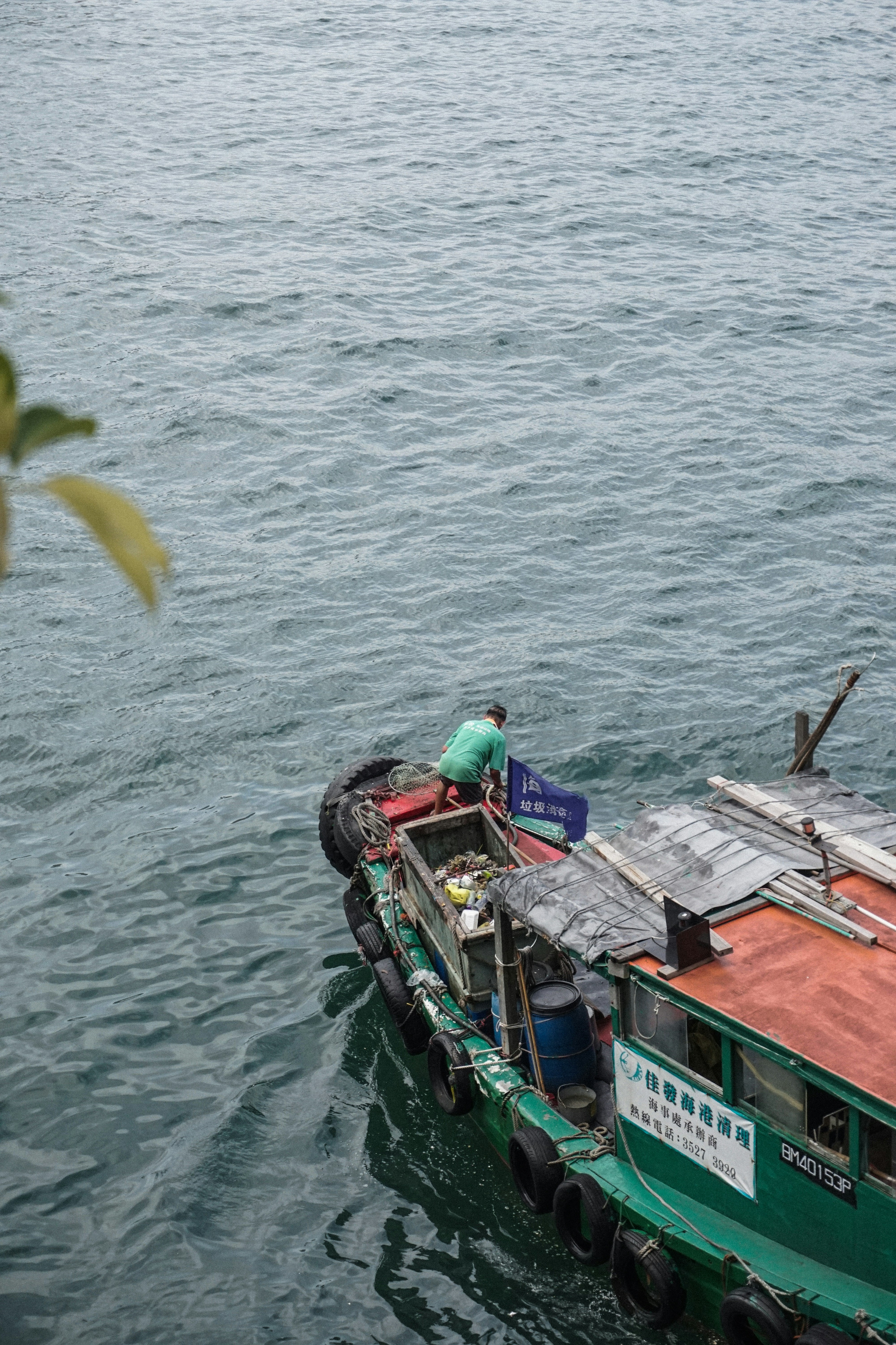 Crewman in Green on a Teal Harbor Boat: A Quiet Moment at Sea