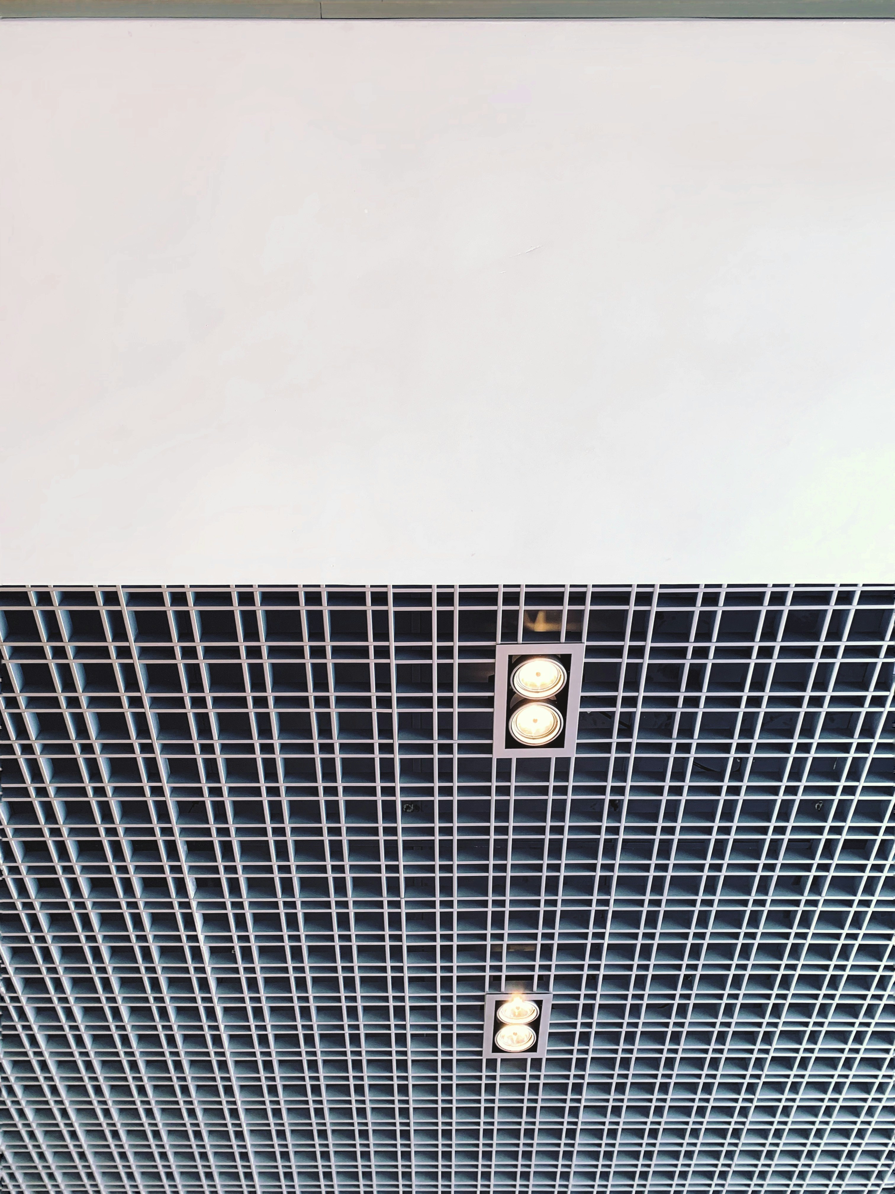 Modern ceiling design featuring a grid pattern with recessed lighting. The interplay of light and shadow creates a visually intriguing effect.