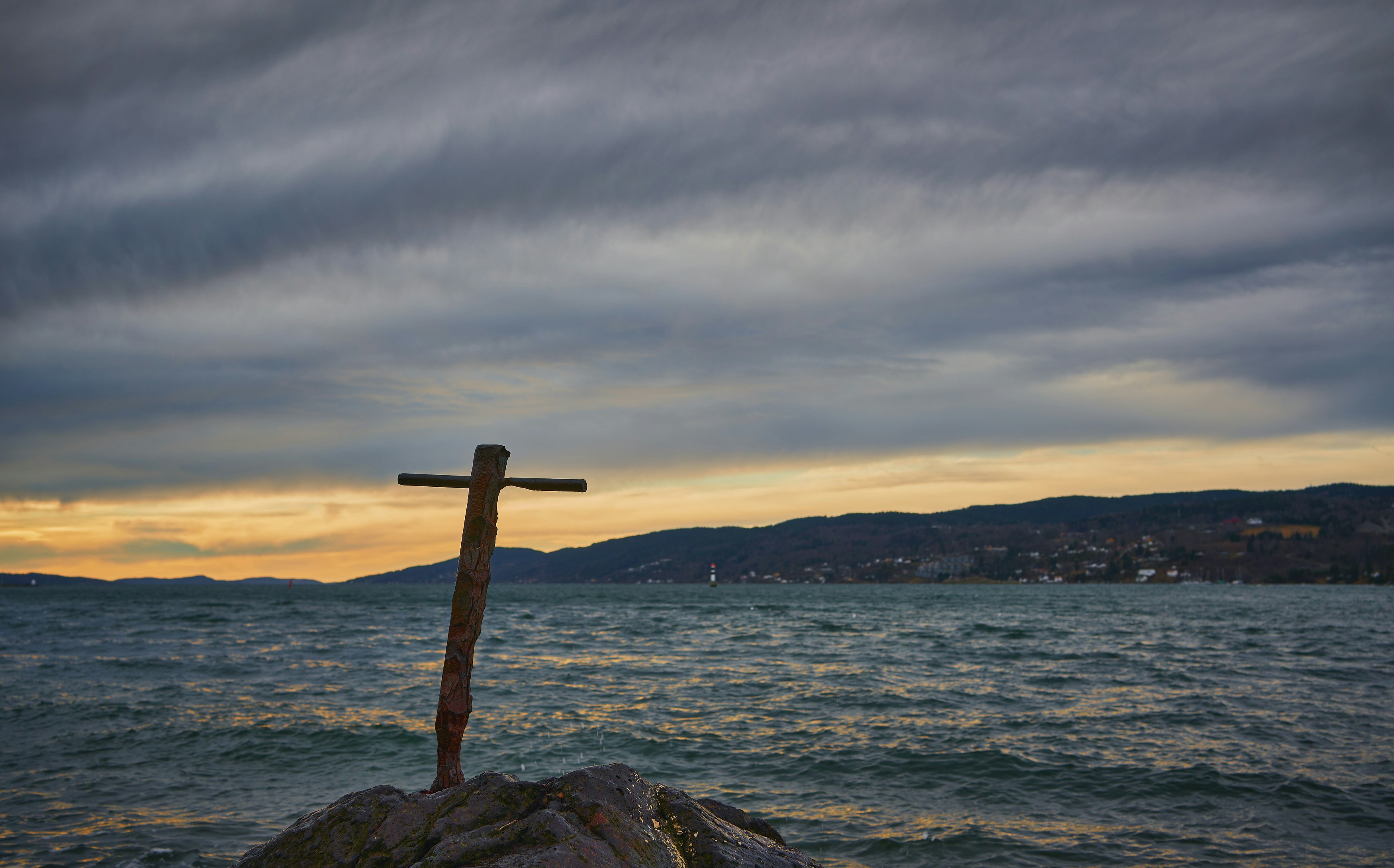 Cross on the Rock: A Weathered Beacon at Sunset Over a Quiet Sea