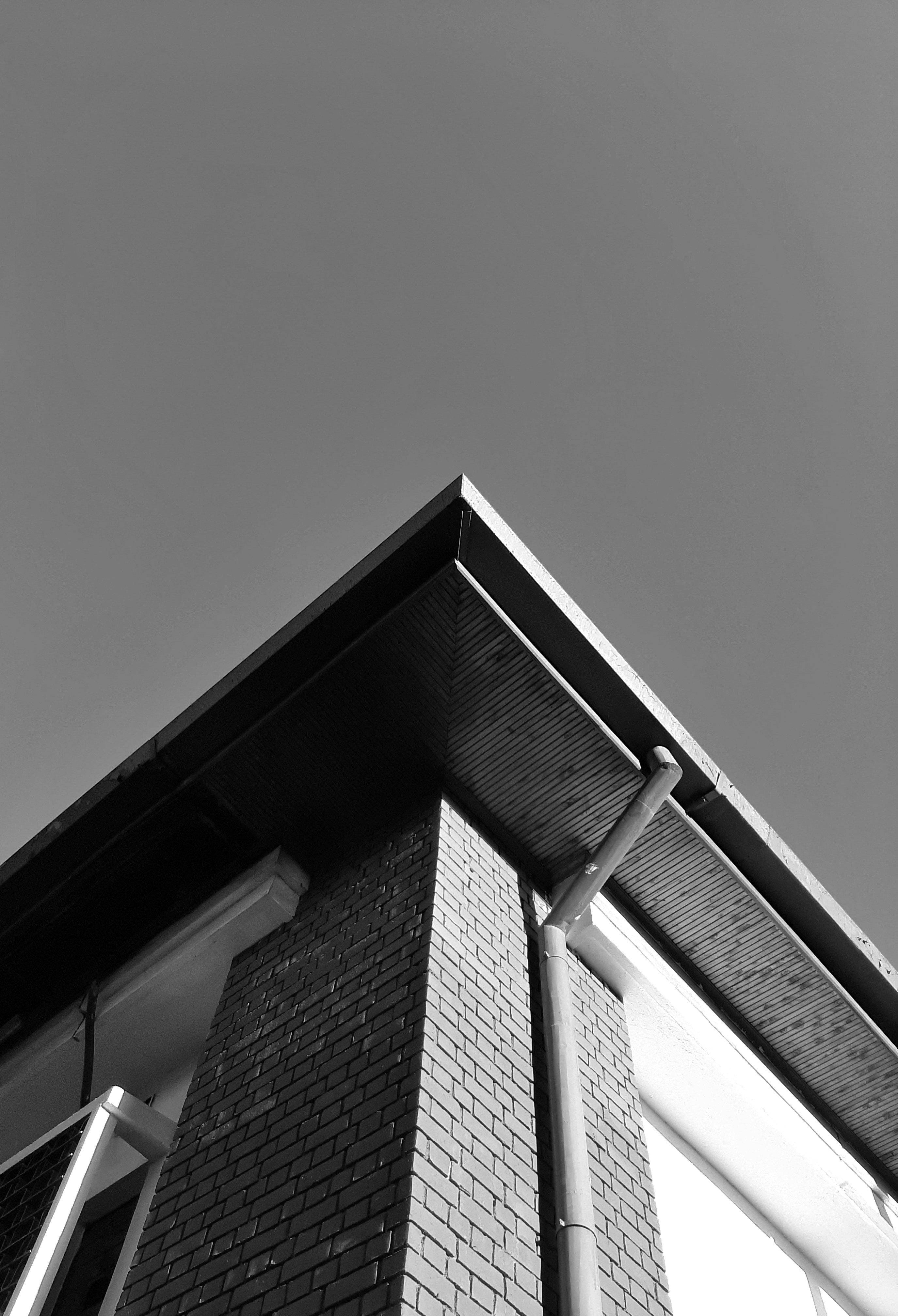 The corner of a brick building meets a clear sky, showcasing geometric lines and contrasting textures in monochrome.