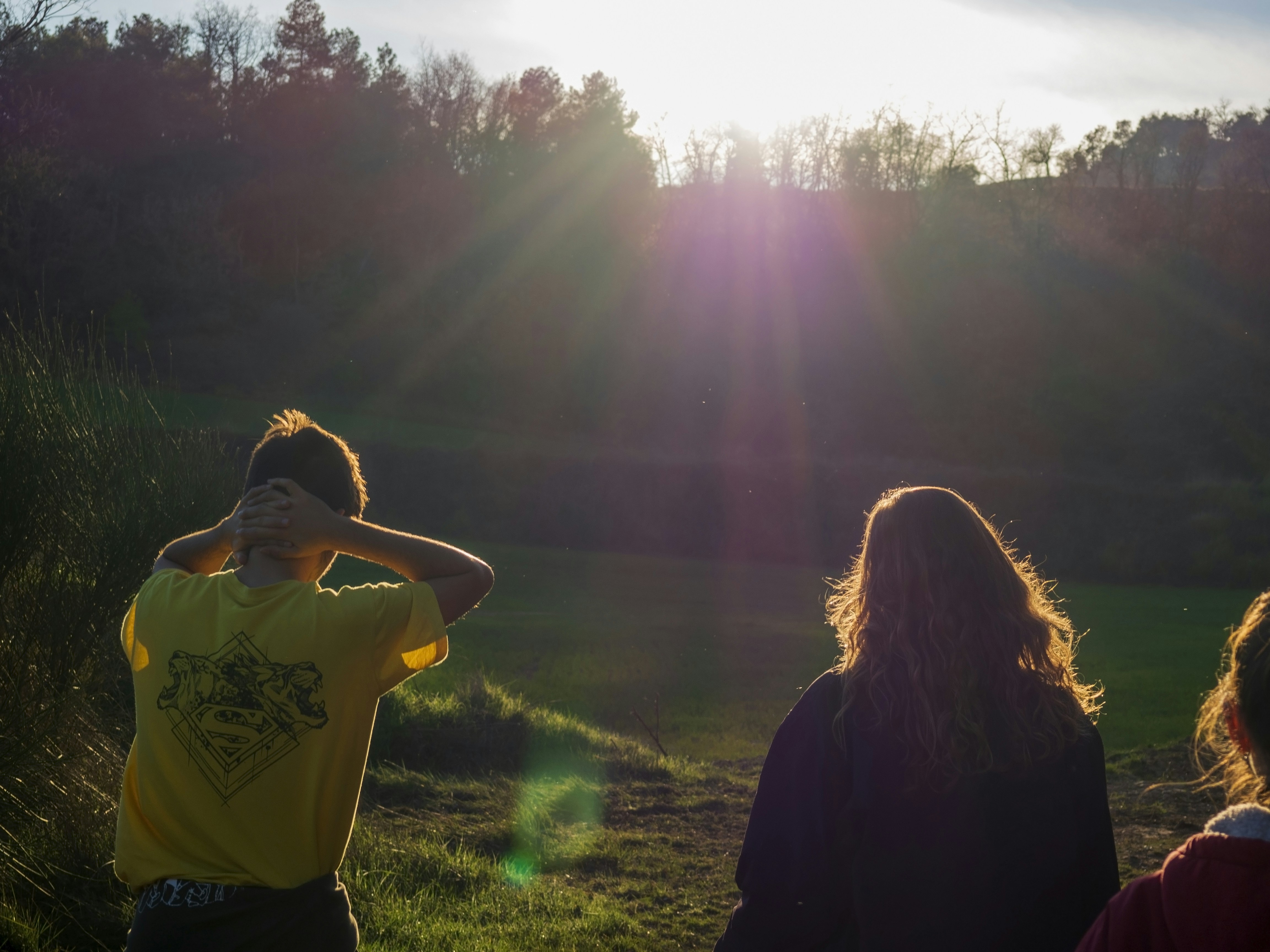 Silhouetted figures stand in contemplation as the sun sets, casting a warm glow over the landscape. The scene evokes a sense of tranquility and reflection.