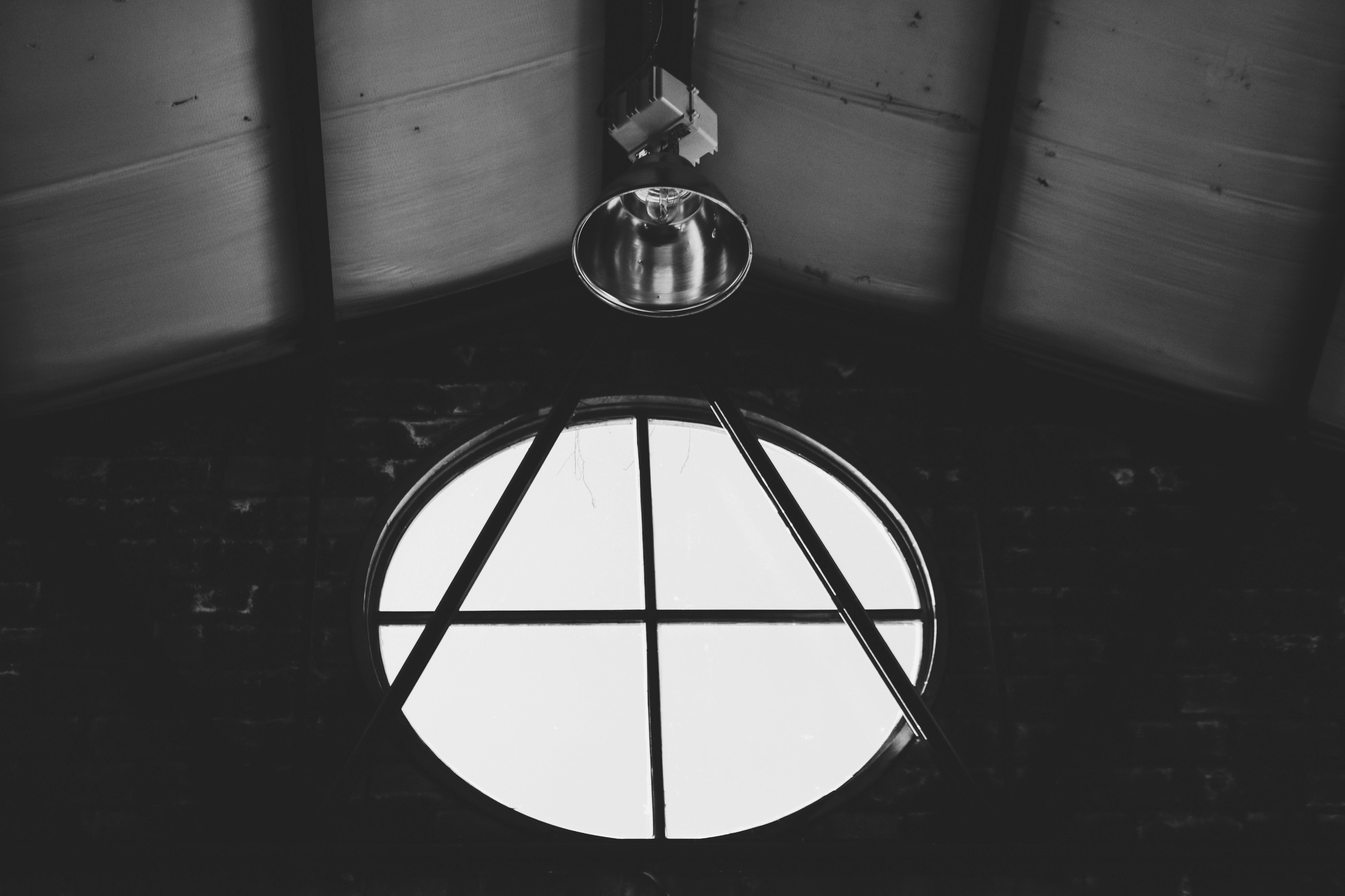 Circular window framed by intersecting beams and a hanging light fixture in a rustic setting.