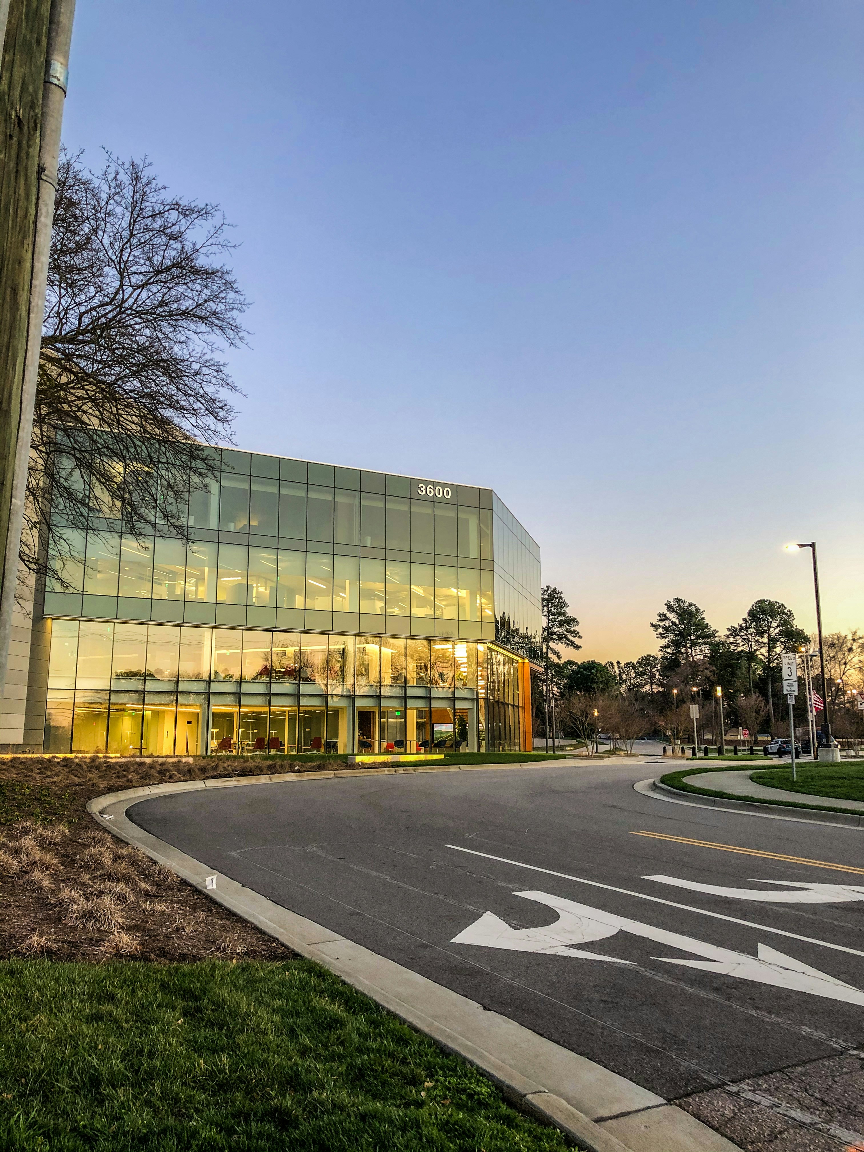 Modern glass building showcasing a reflective facade with trees and a winding road in the foreground.