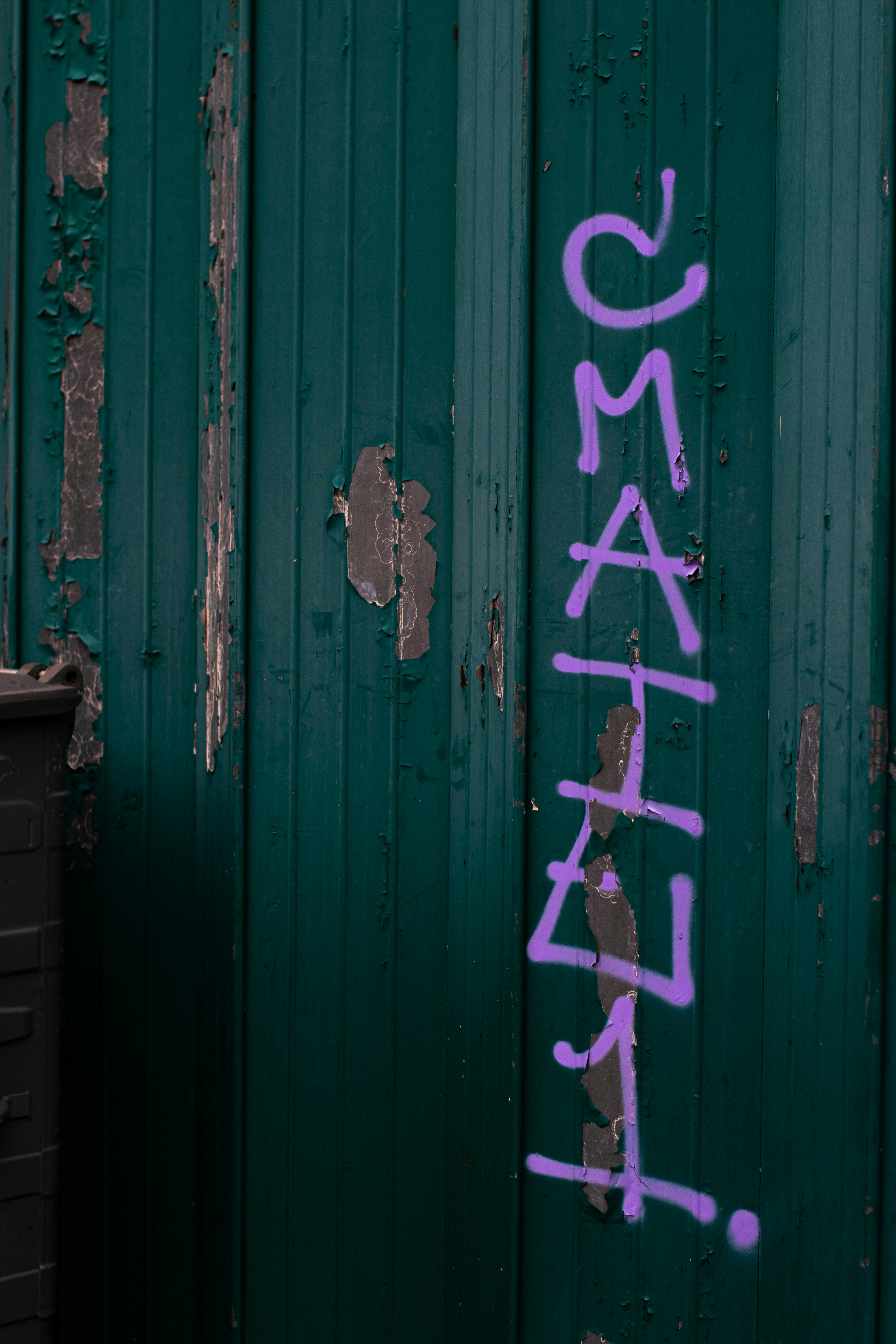 Vertical graffiti on a peeling teal metal wall