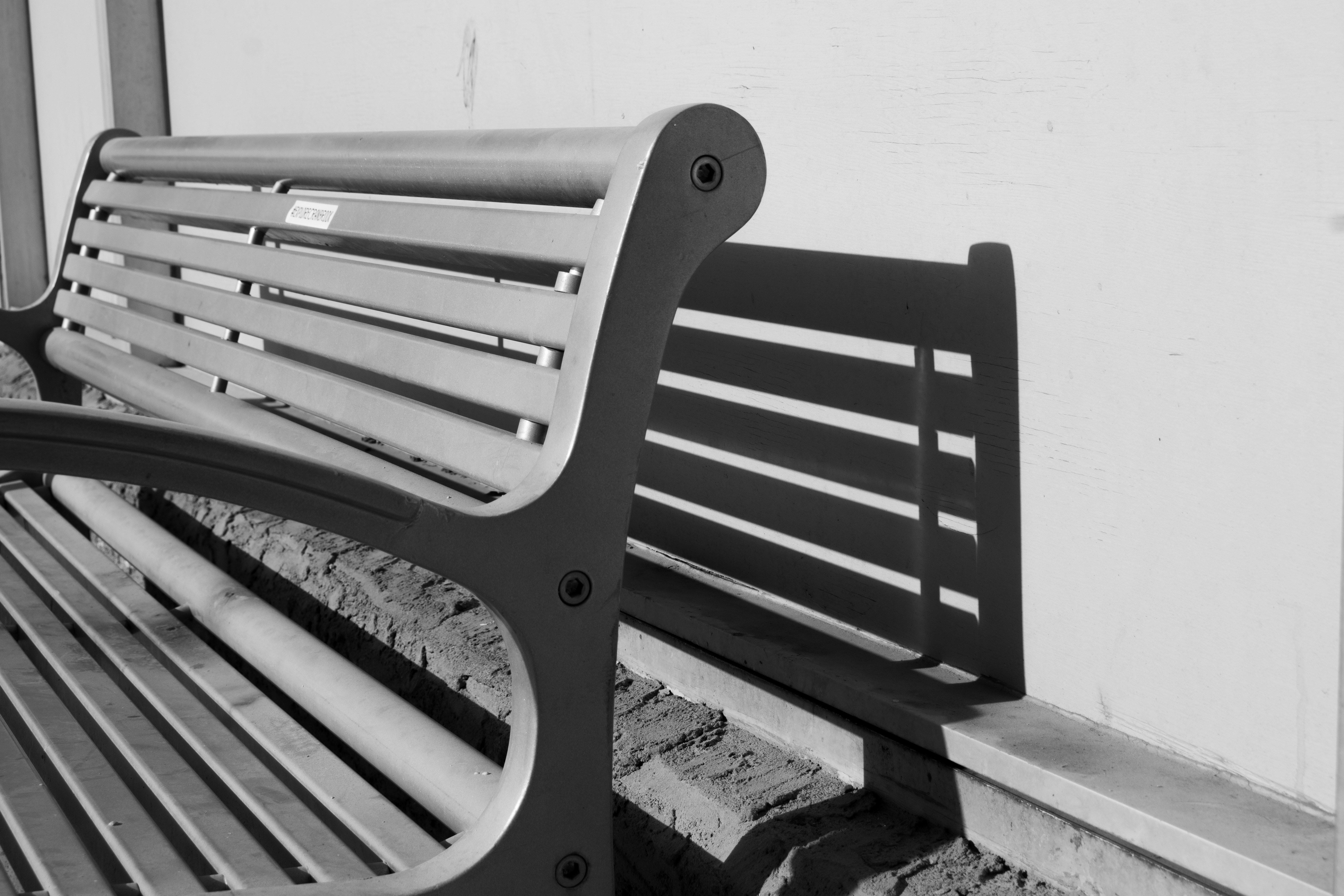 A modern bench casts intricate shadows against a textured wall, highlighting the interplay of light and form.