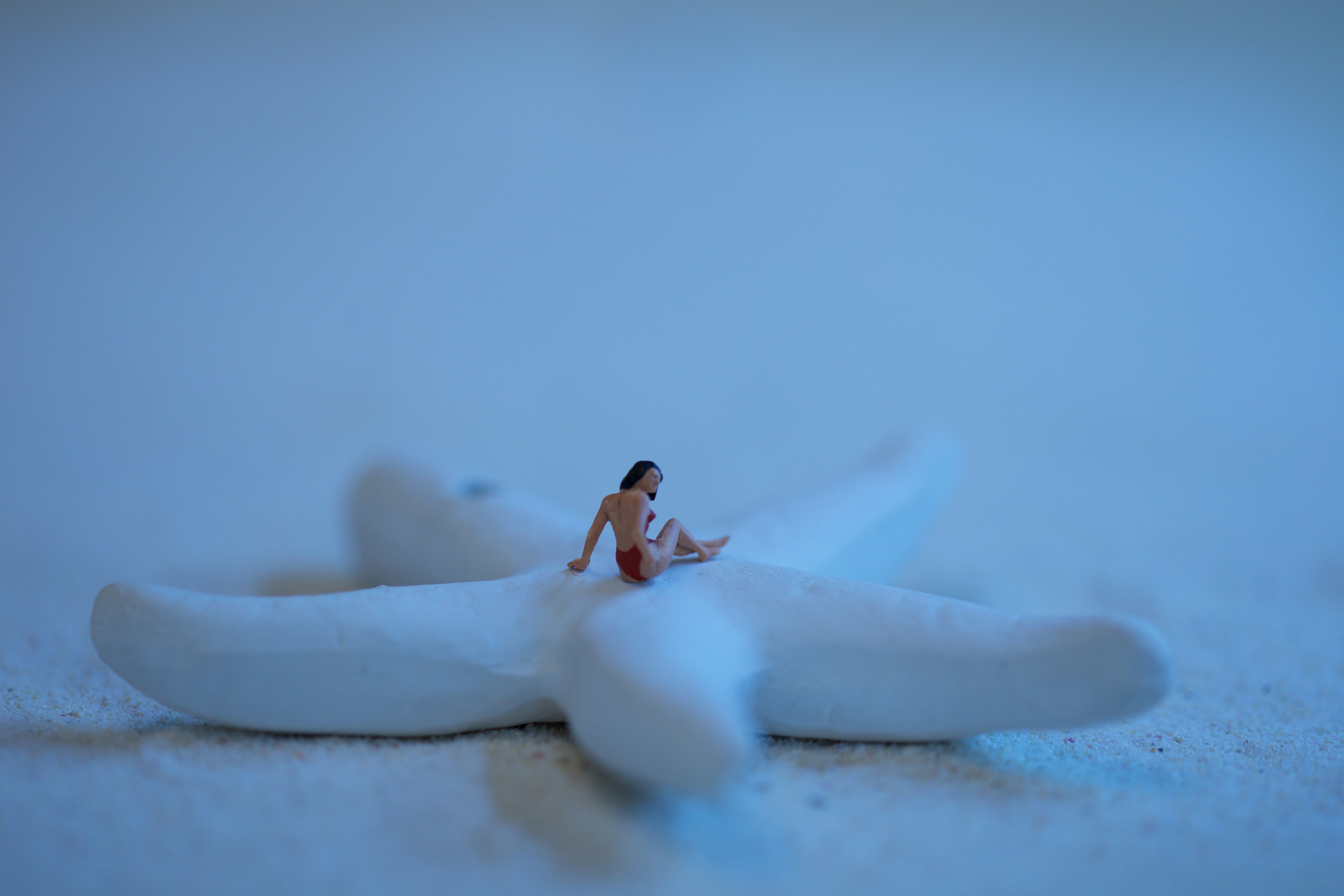 Miniature figure lounging on a white starfish against a soft blue background, evoking a sense of tranquility and whimsy.