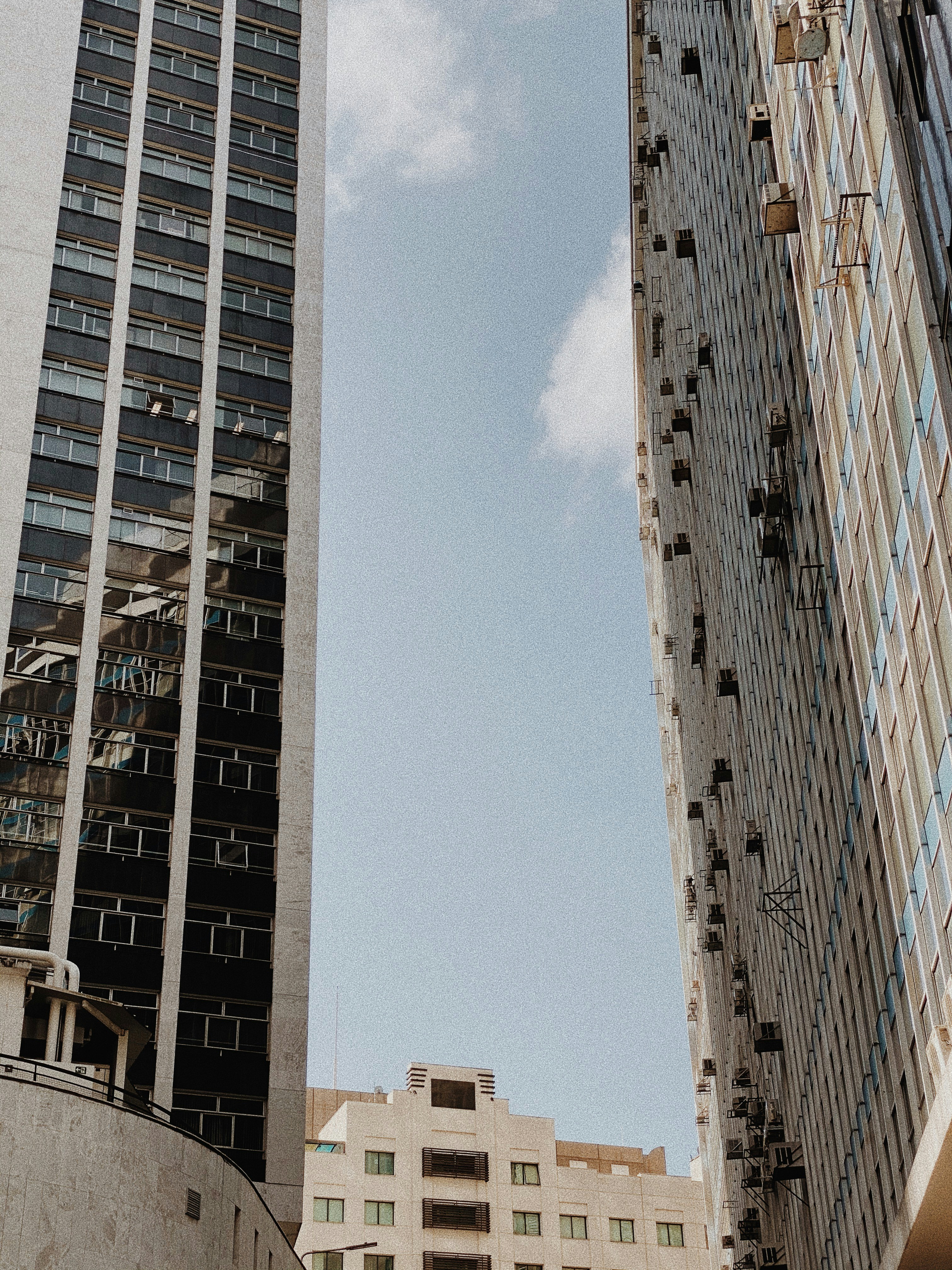 Tall skyscrapers framing a patch of blue sky with scattered clouds.